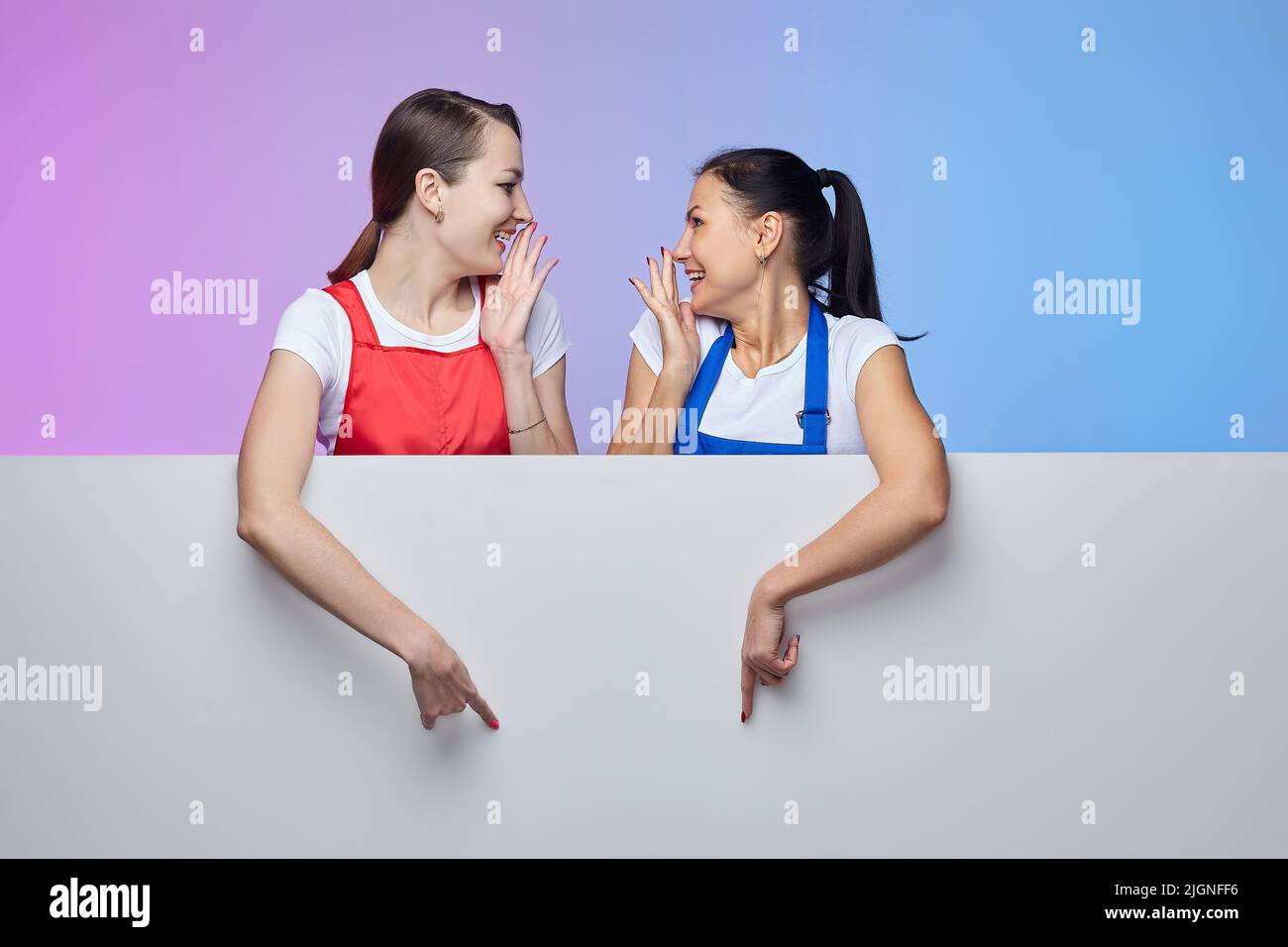 two girls in aprons pose with a white Billboard. advertising concept ...
