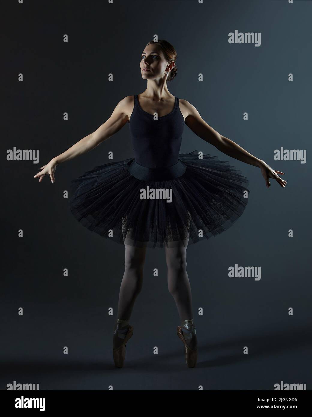 attractive ballerina poses gracefully in the studio on a black ...
