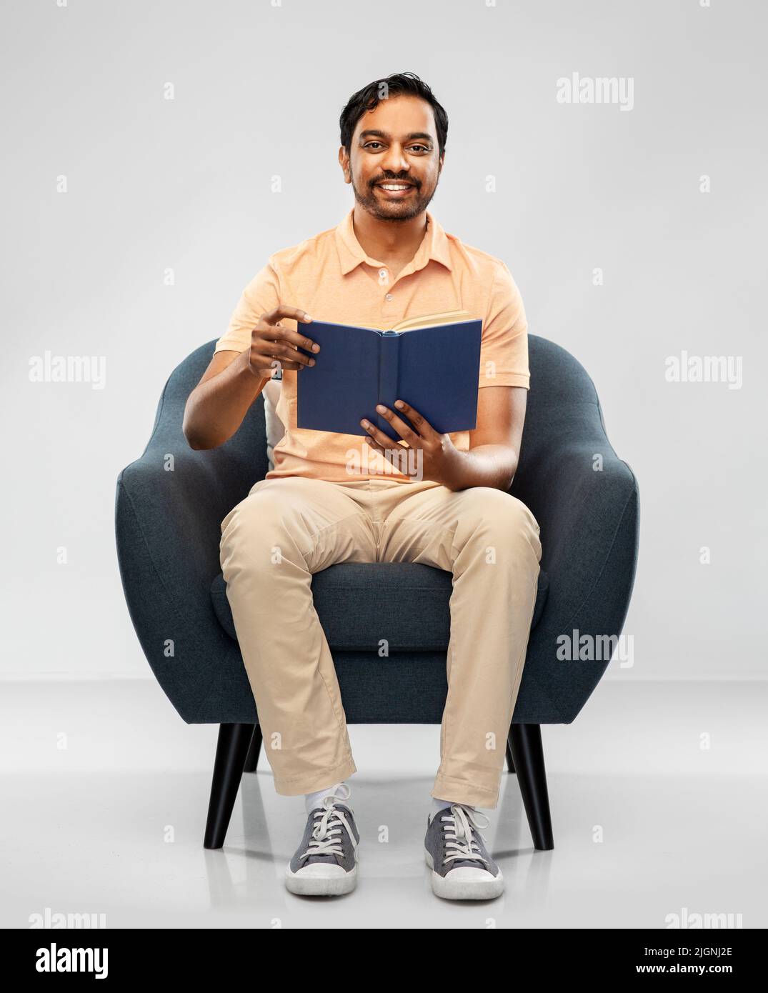 happy young indian man reading book in chair Stock Photo - Alamy