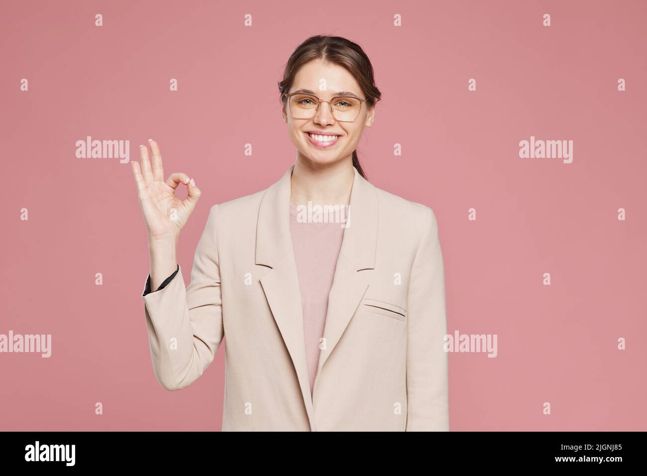 Portrait of smiling female manager in eyeglasses standing against pink ...