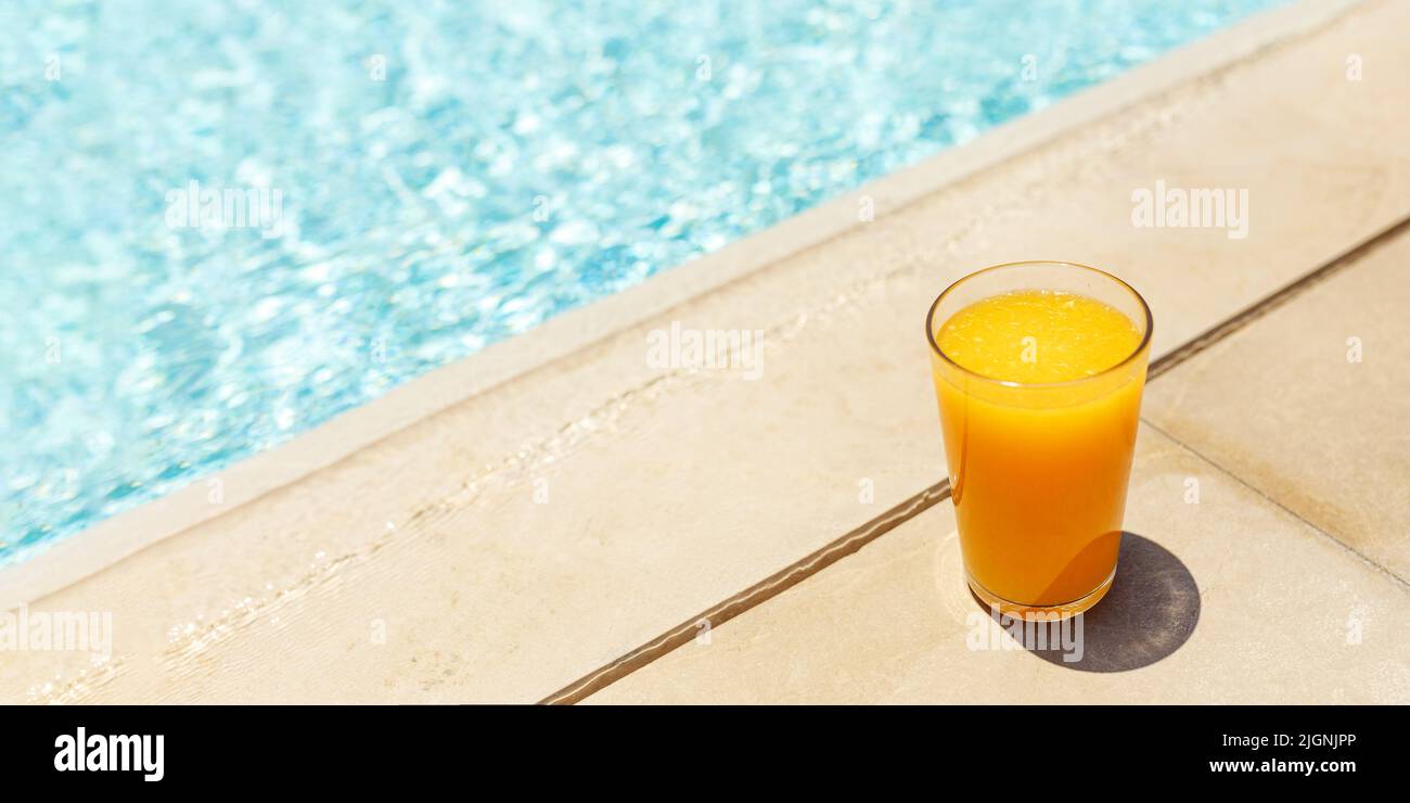 Glass of fresh cool orange juice drink on swimming pool board, summer tropical holiday concept ...