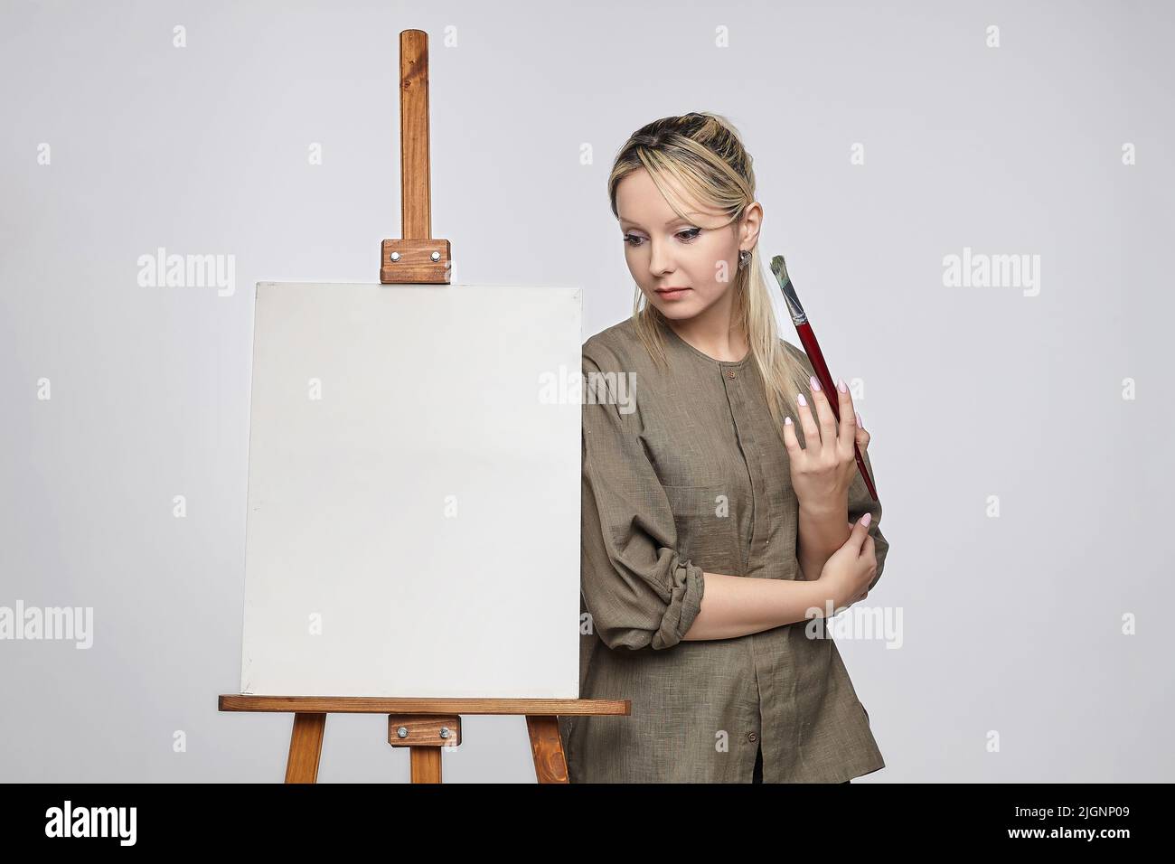 young female artist stands in front of an empty canvas wondering what ...