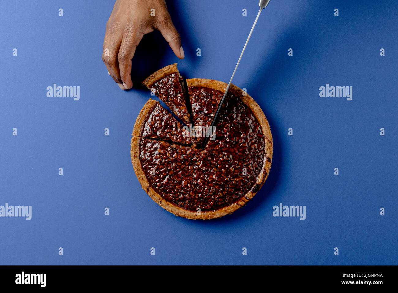 Composition of hands of biracial man cutting pie with knife on blue ...