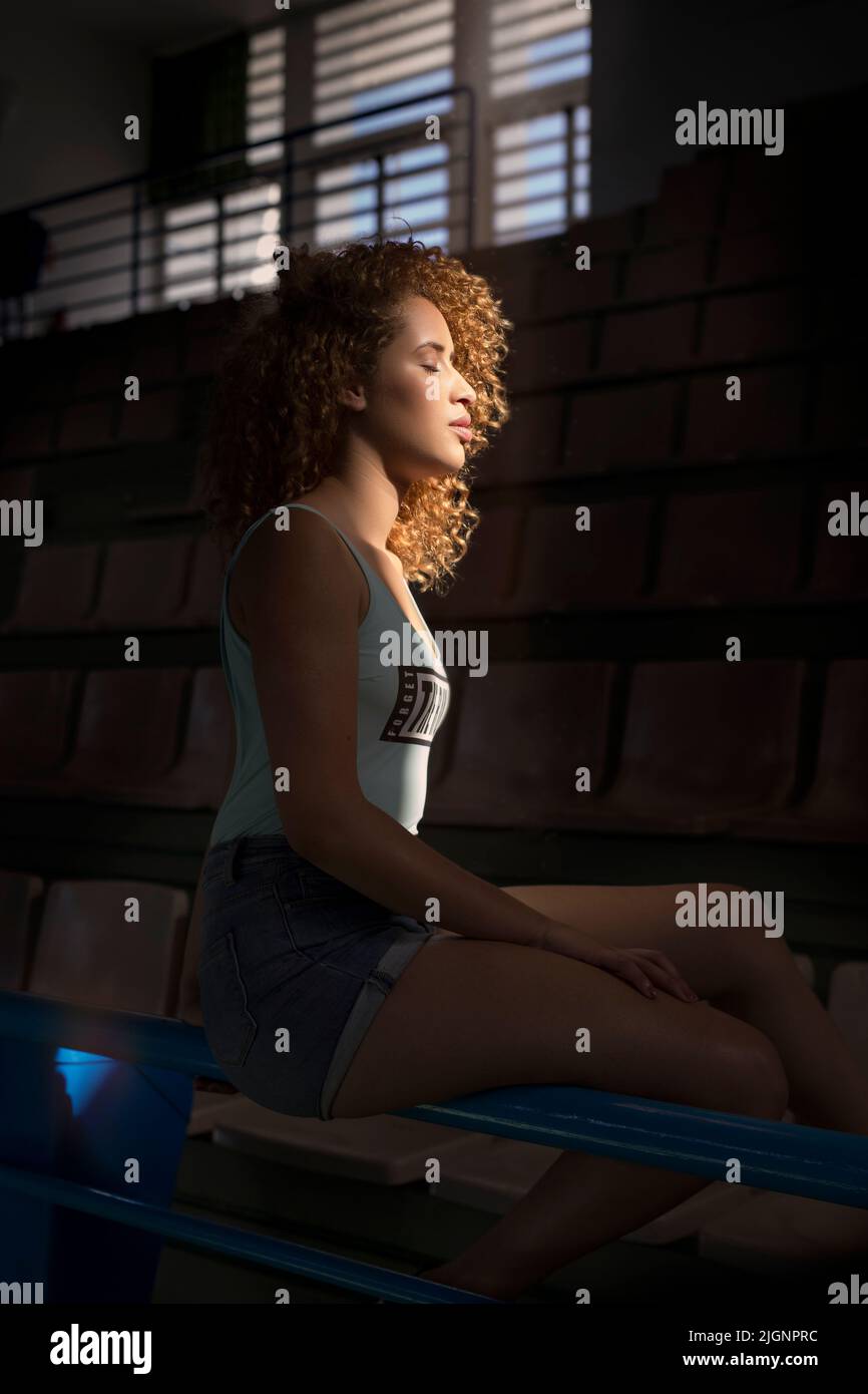 Side view of tranquil female with curly hair in denim shorts sitting ...