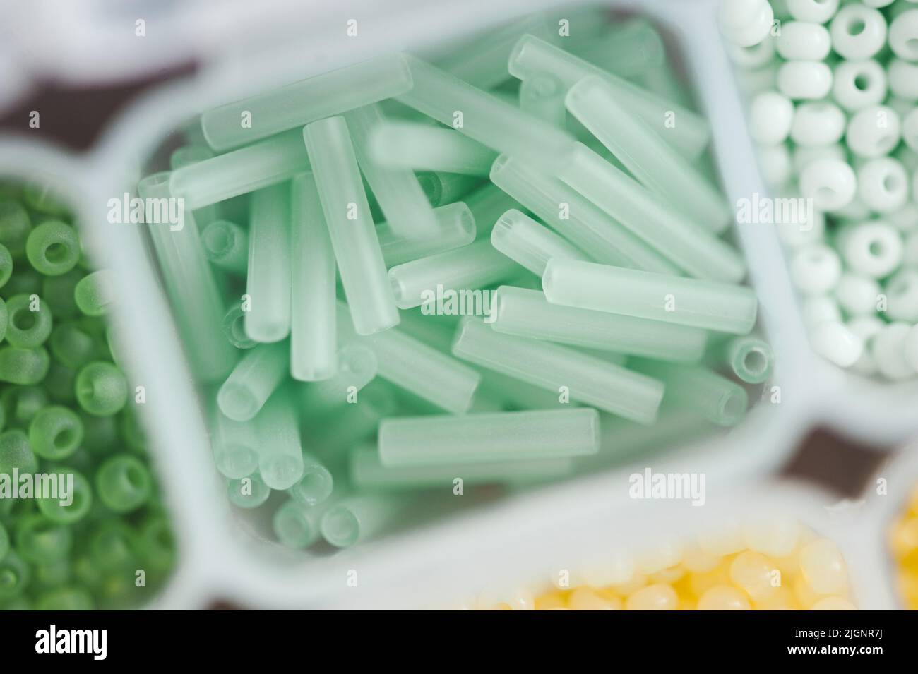 Small tiny colorful glass beads in plastic box container close up top ...