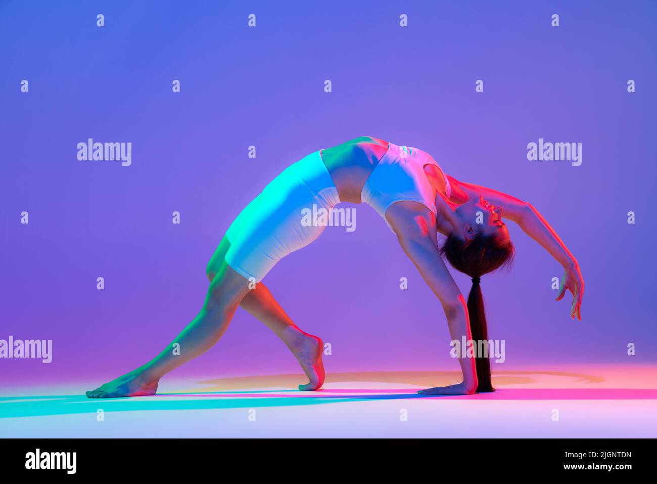 Studio shot of young flexible girl in fitness sport uniform practicing ...