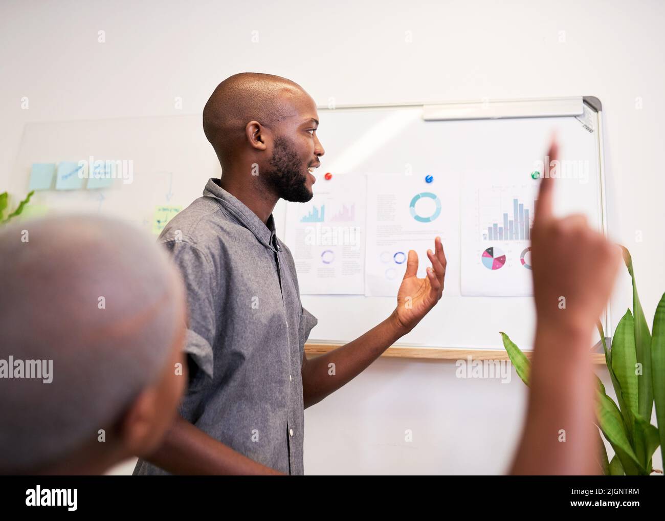 A Black man gives a presentation in the office while a colleague asks a ...