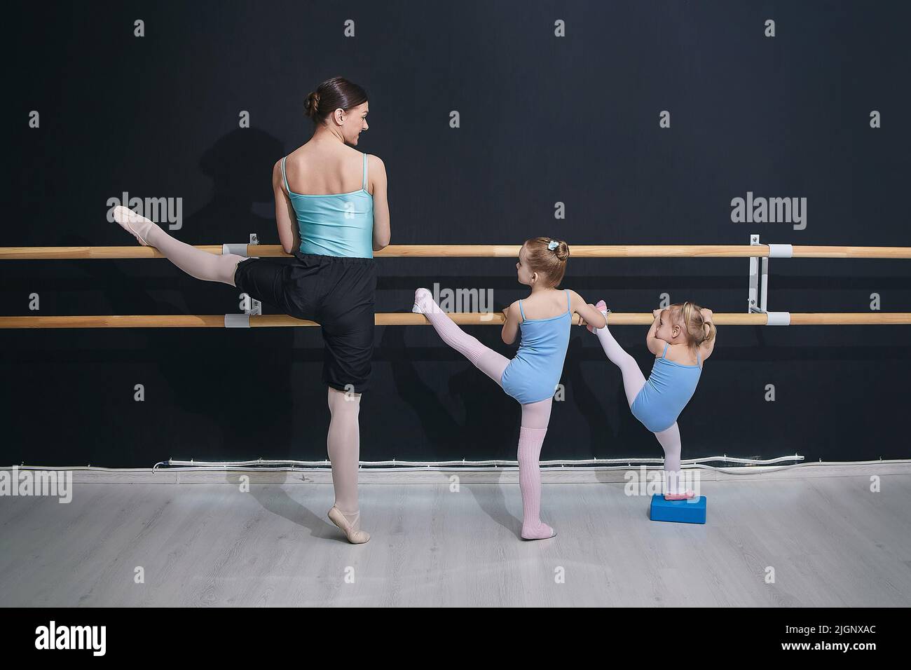 two little girls repeat the exercises after the teacher on the barre ...