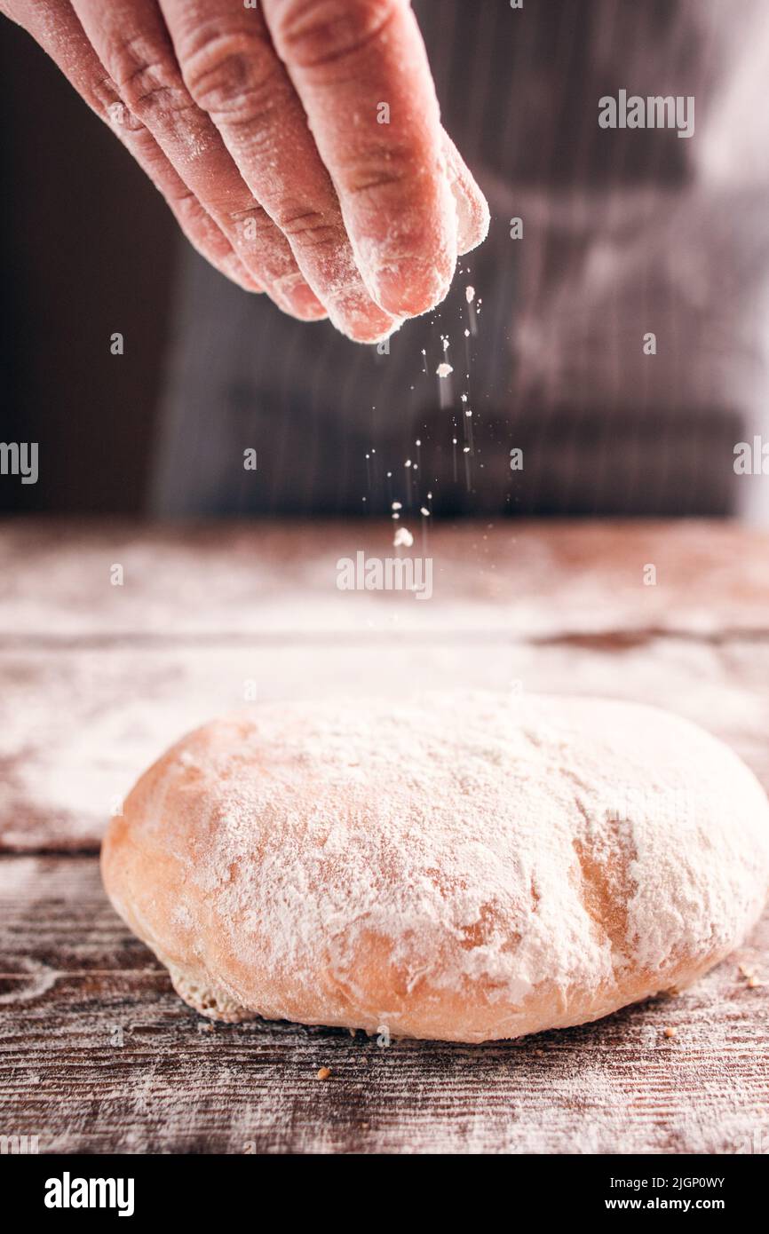 Baker hand sprinkling flour on fresh warm bread Stock Photo - Alamy