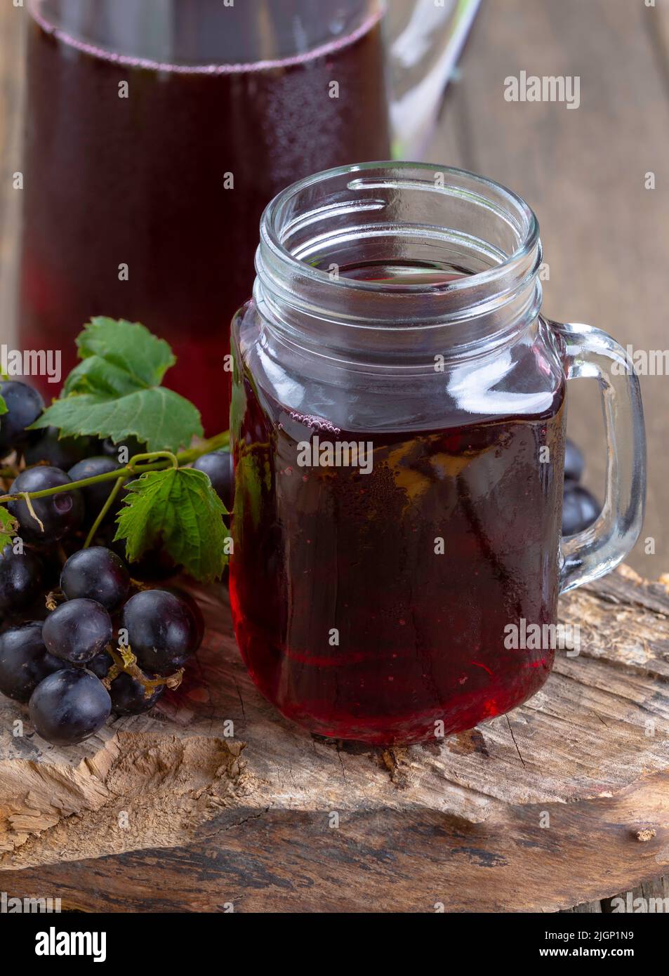 Glass of grape juice with fresh grapes on a wooden block with pitcher ...
