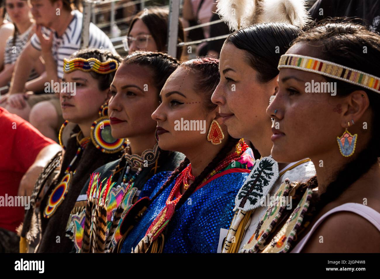Pow-wow dancers wearing traditional costumes watch the presentation ...