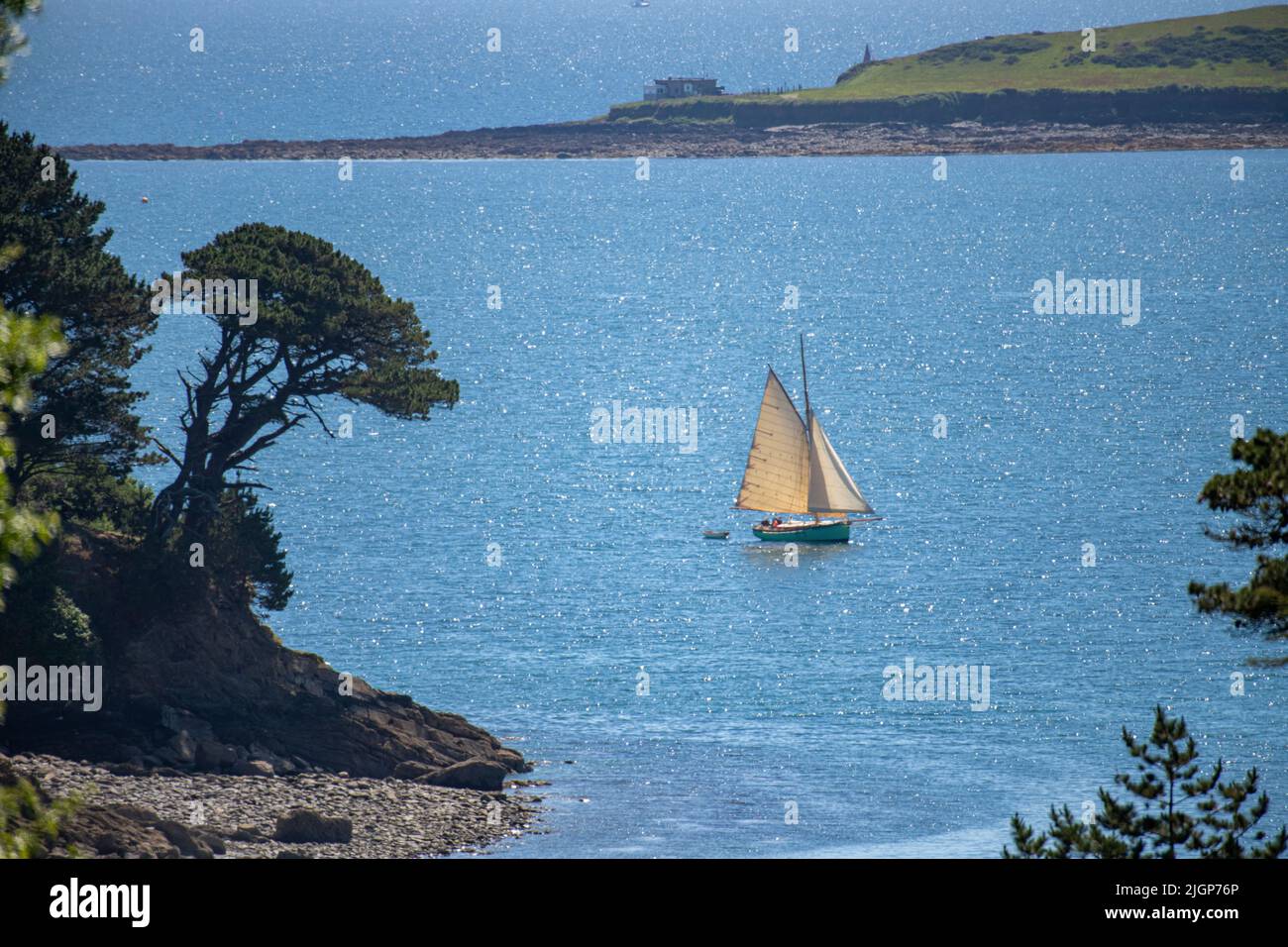 A classic sailing boat sails in glistening waters towards Cow's Beach ...