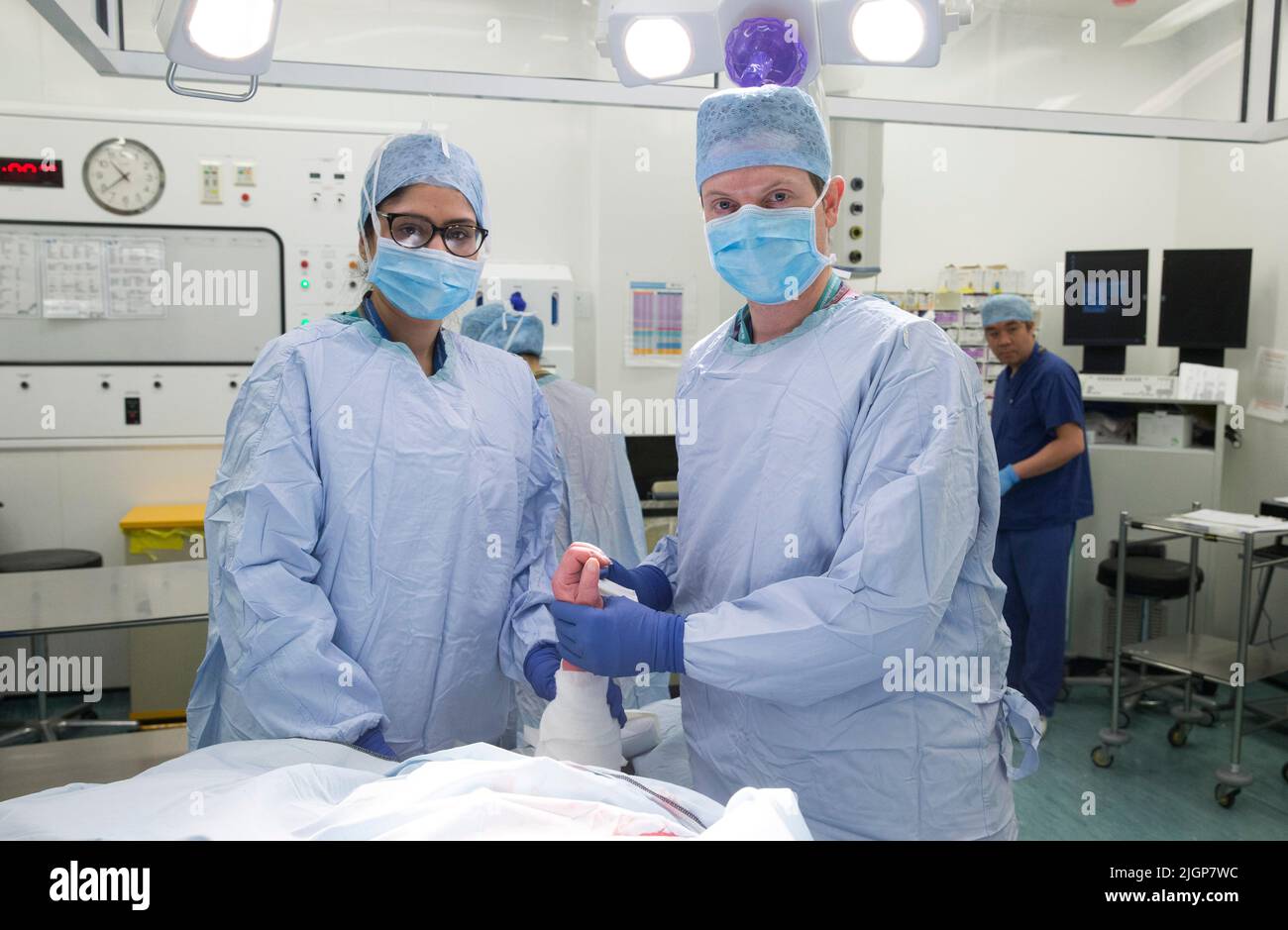 Two surgeons perform an operation on the arm of a patient in an NHS ...