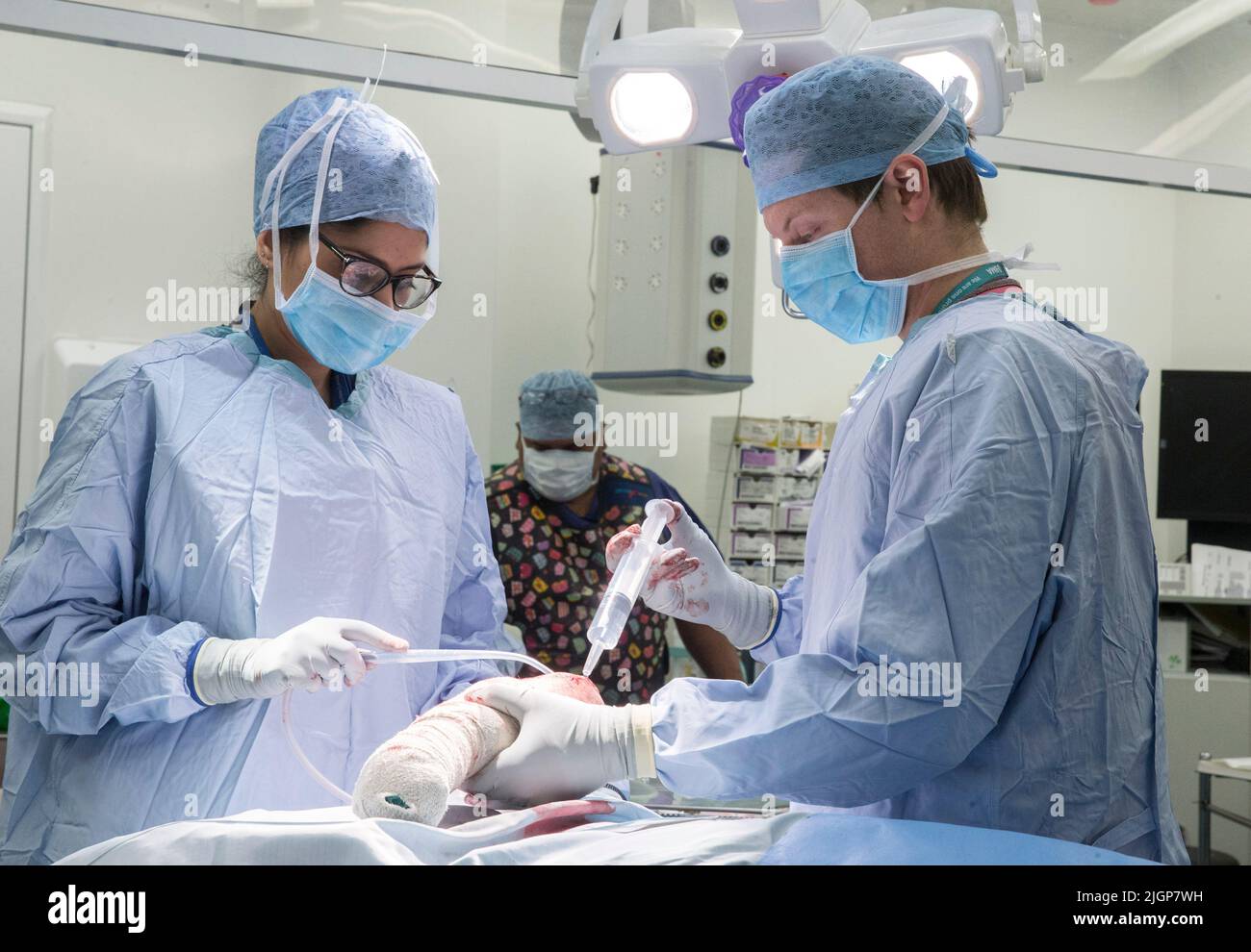 Two surgeons perform an operation on the arm of a patient in an NHS ...