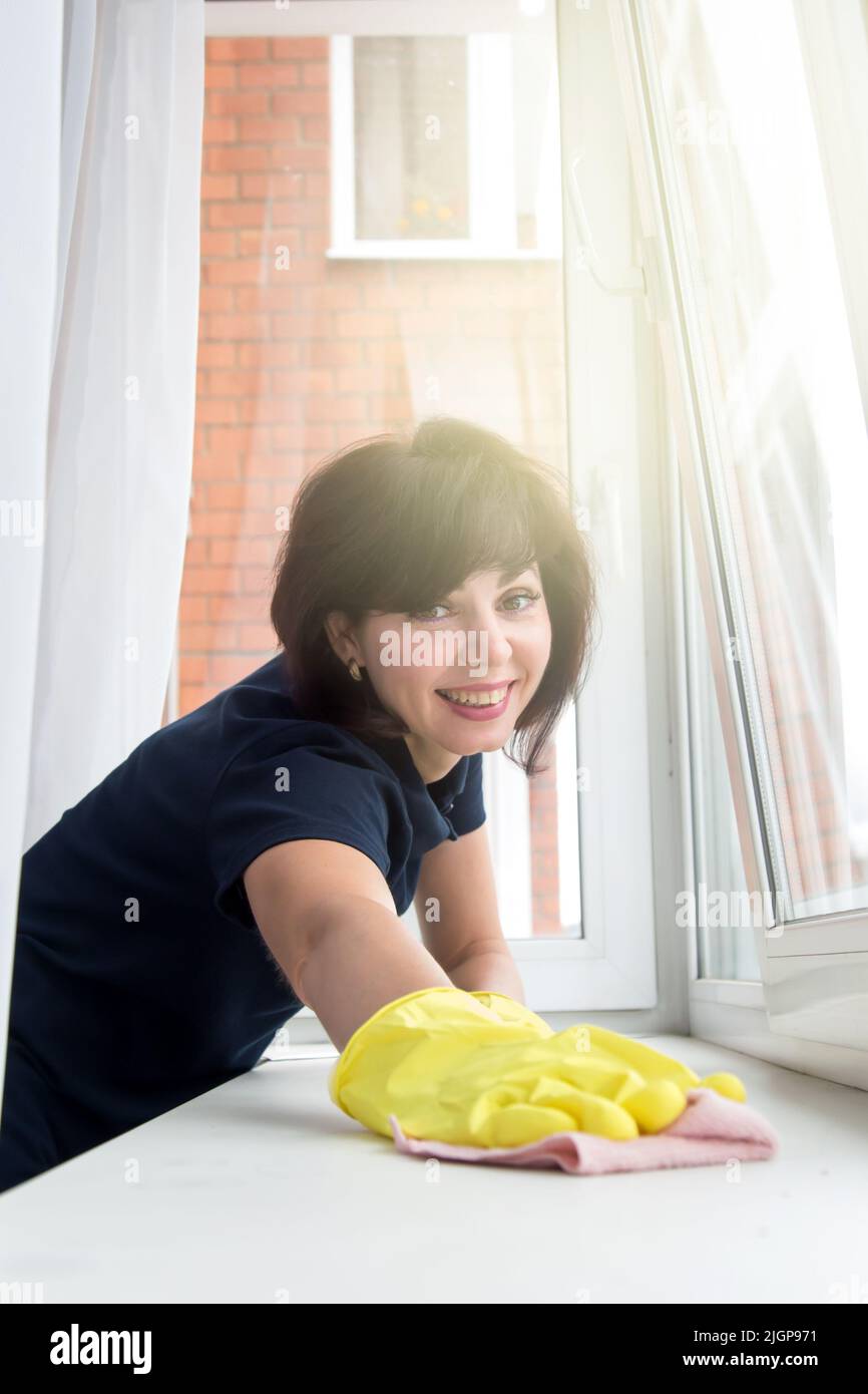 Beautiful woman with a smile wipes the window from dust on a summer day ...
