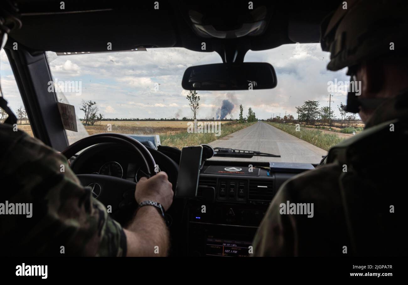 People in camouflage uniforms in a car on the road among burning fields ...