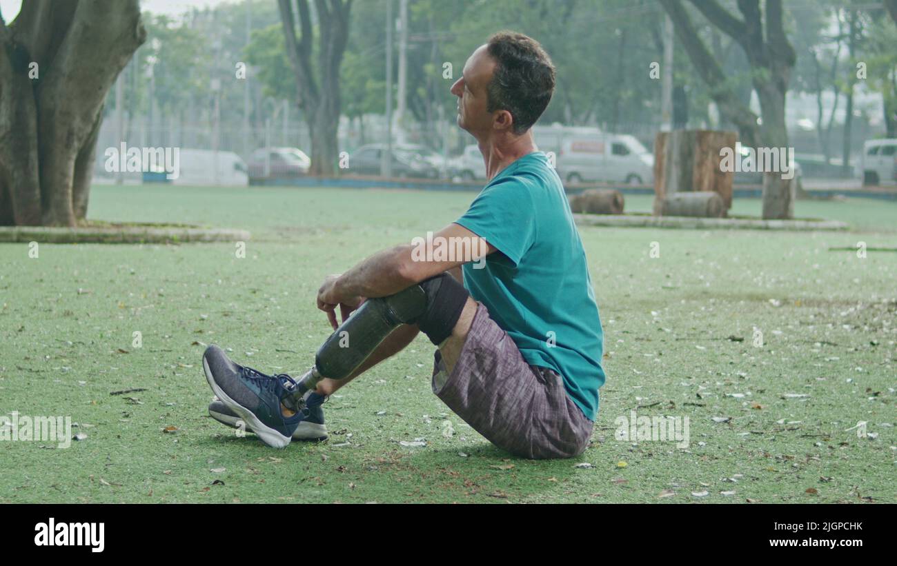 One disabled man with prosthetic leg stretching outside after sport ...