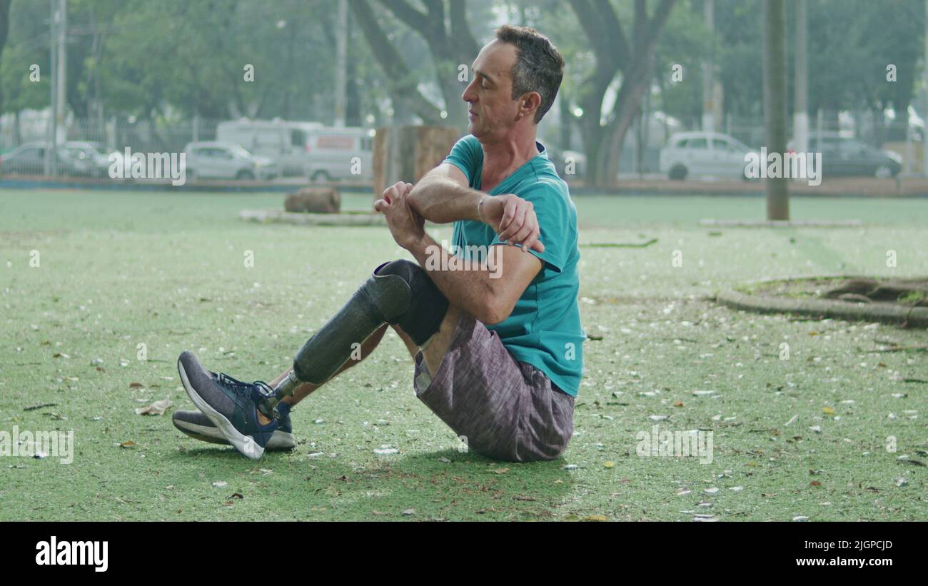 One disabled man with prosthetic leg stretching outside after sport ...