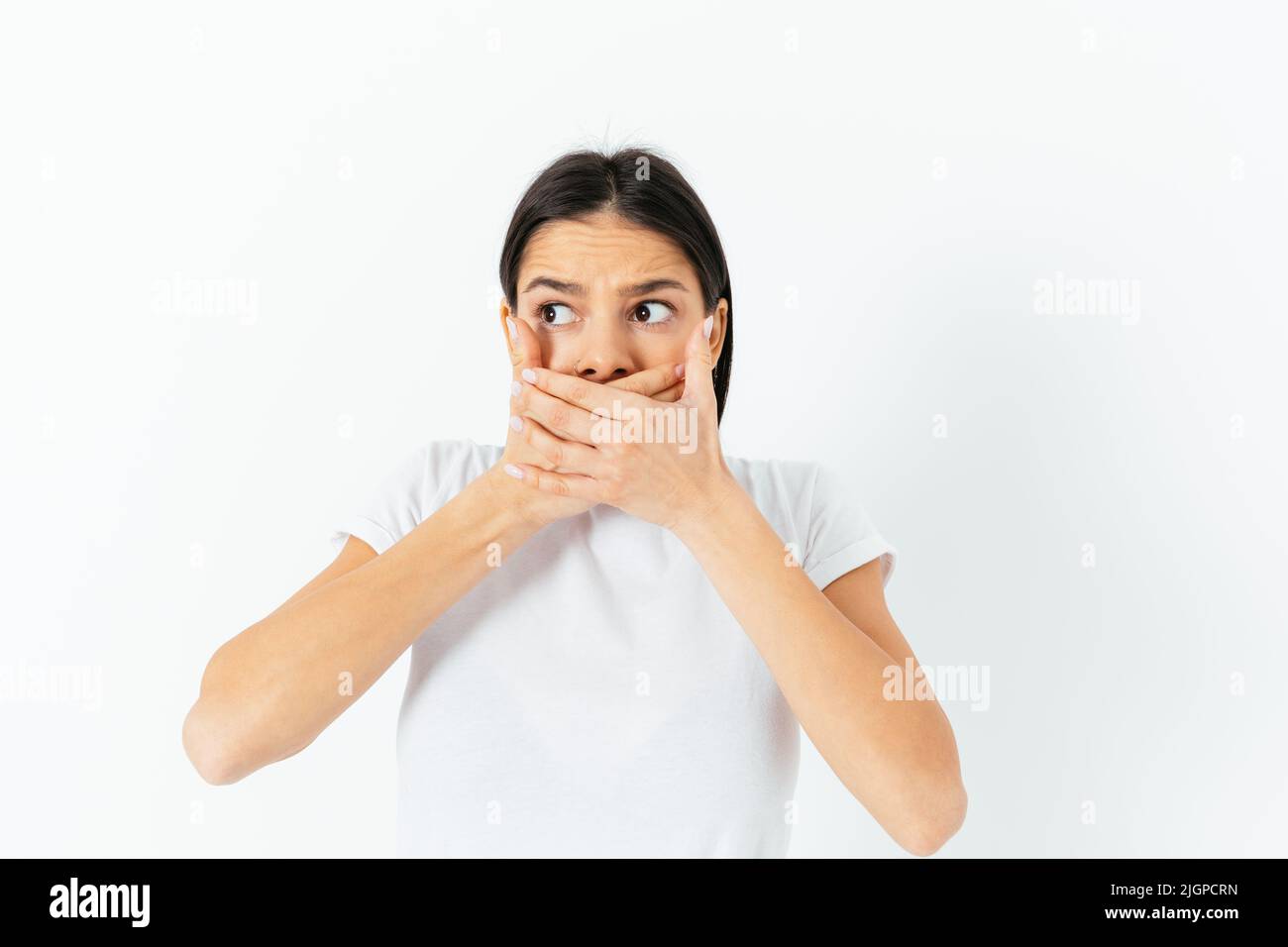 Worried young brunette woman covers her mouth with her hands timidly ...