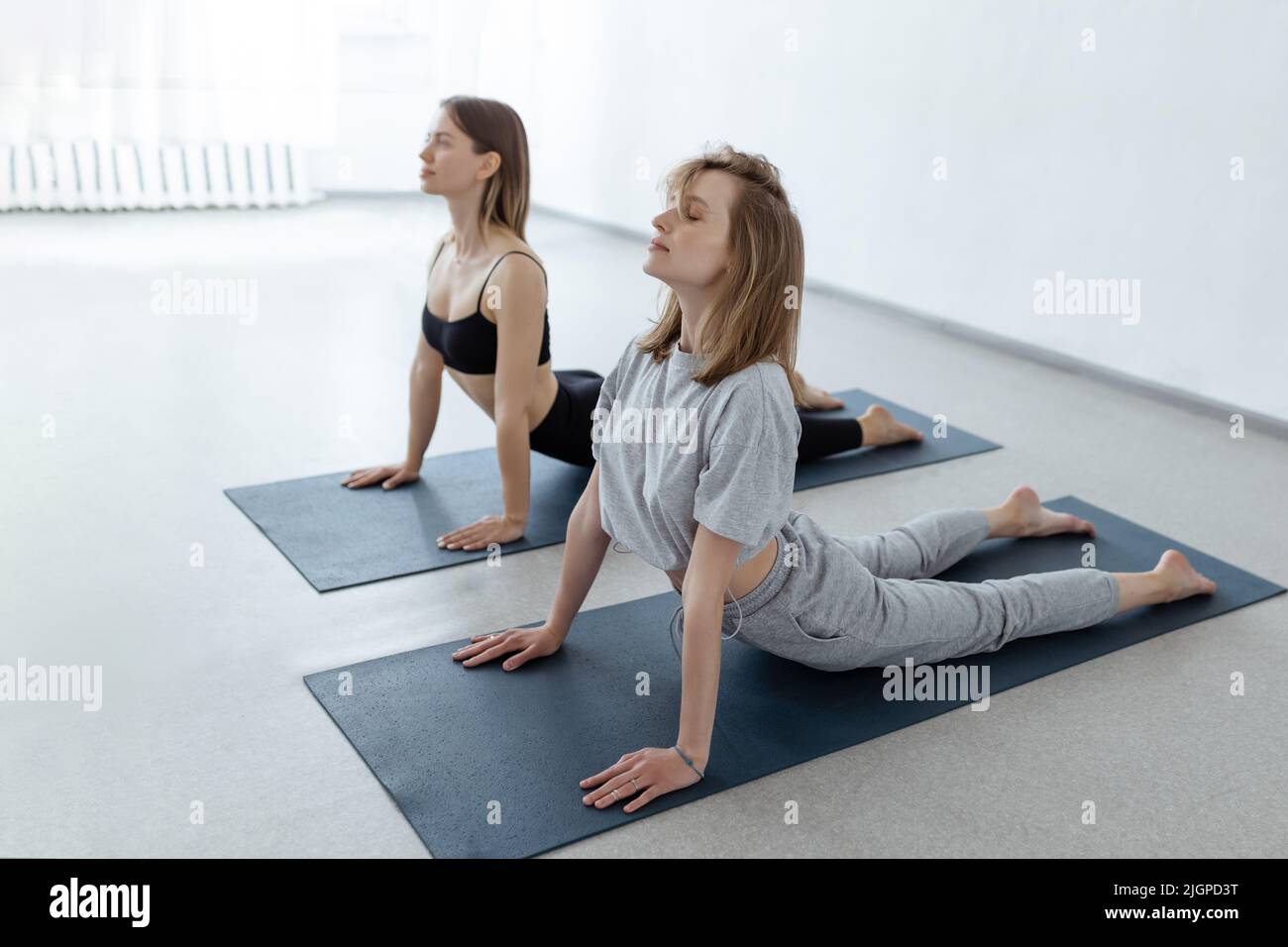 Young girls on yoga training indoors. Attractive girls practice cobra asana in class. Calmness ...