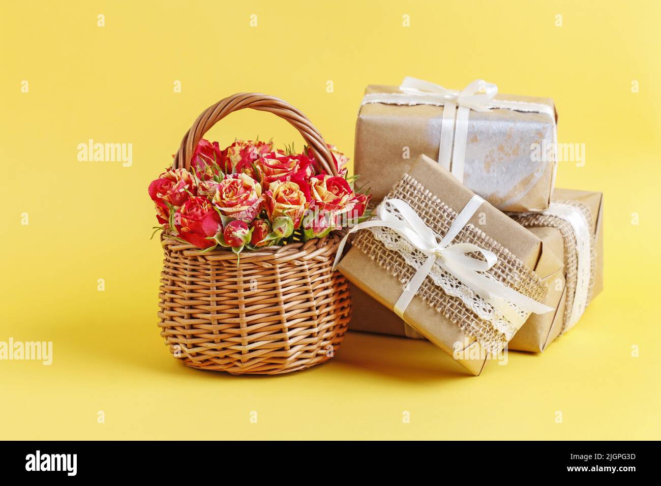 Wicker basket with roses and beautifully wrapped gifts on yellow ...