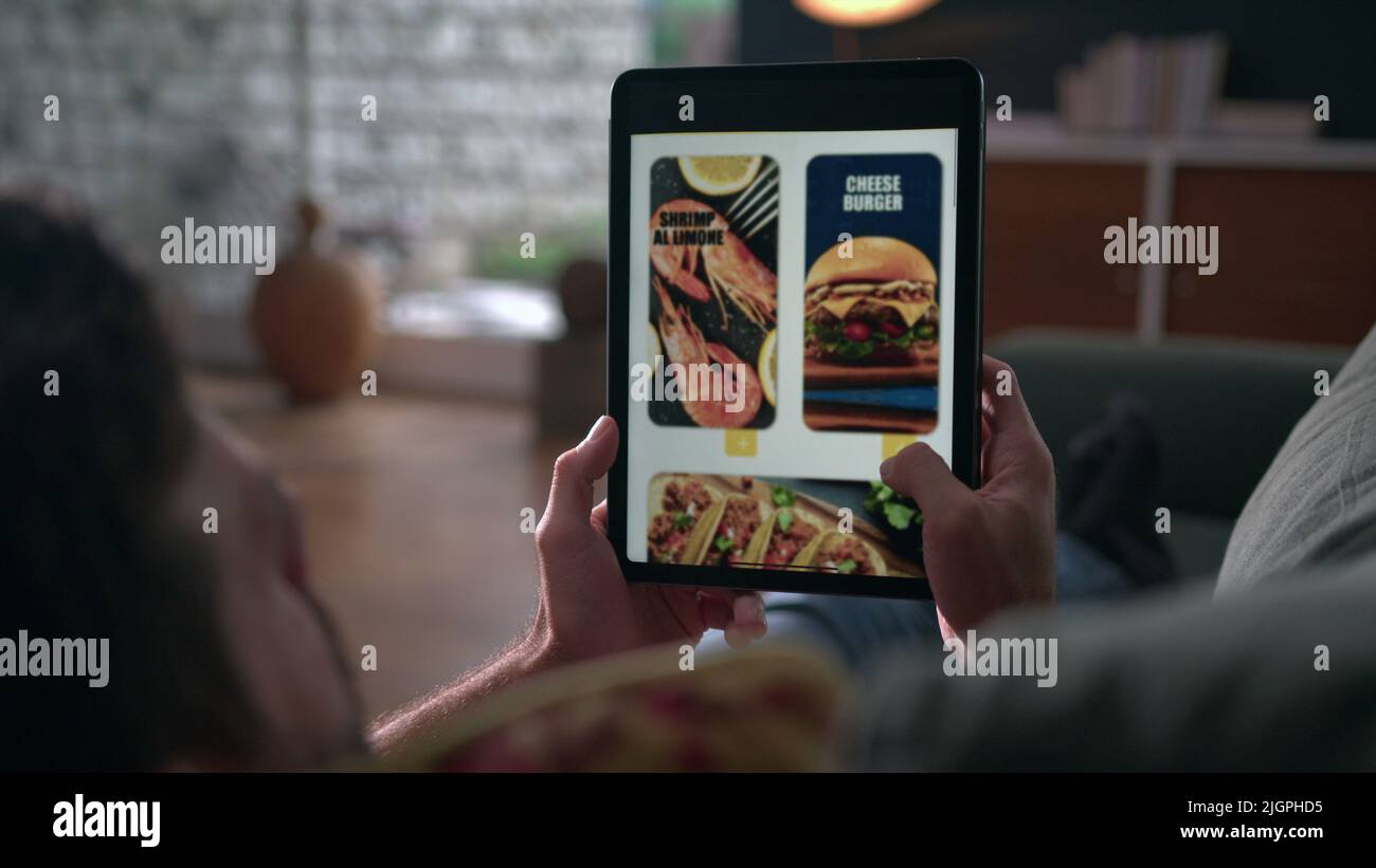 Person scrolling online food menu on tablet device laid on couch at ...