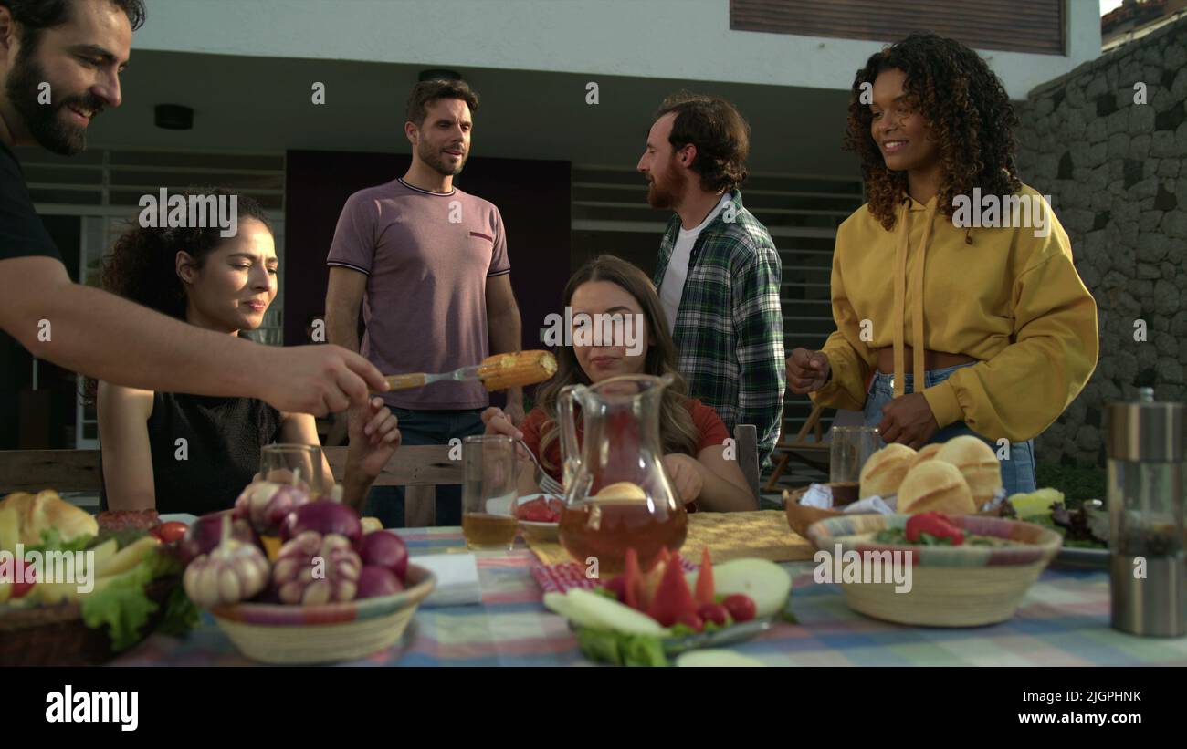 Friends having barbecue. BBQ Chef bringing corn. People gathered ...