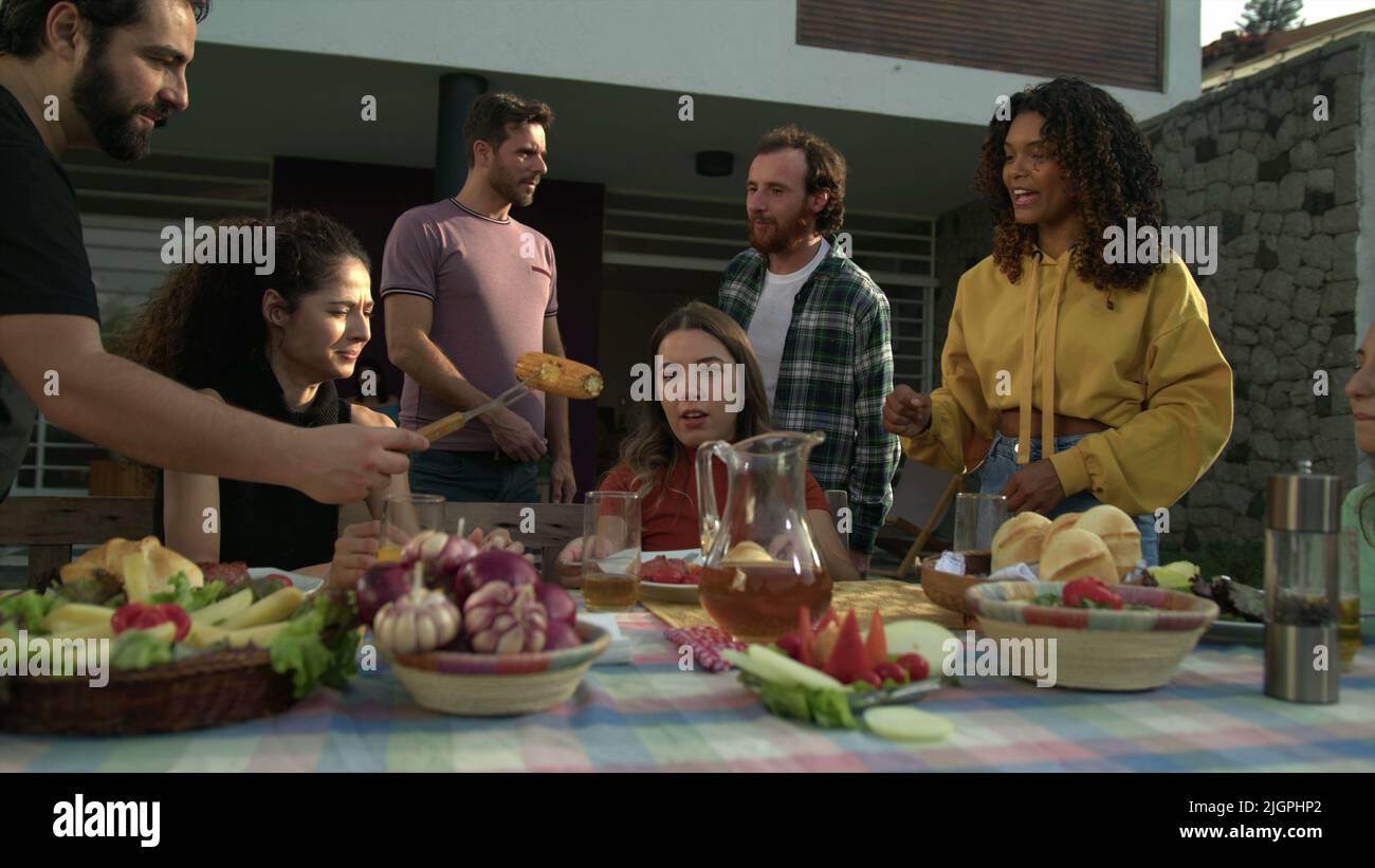 Friends having barbecue. BBQ Chef bringing corn. People gathered ...