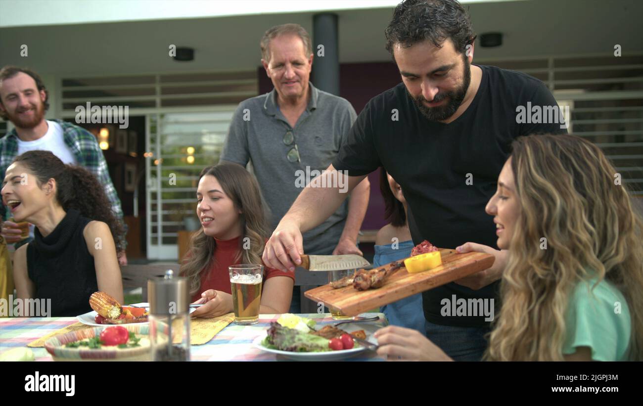Group of cheerful friends eating barbecue together. BBQ chef serving food to friend. People ...
