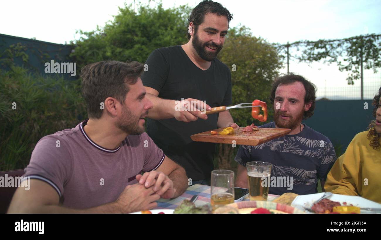 Group of cheerful friends eating barbecue together. BBQ chef serving ...