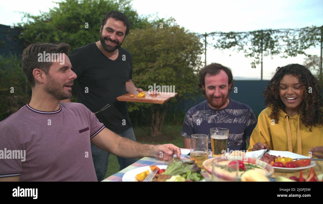 Group of cheerful friends eating barbecue together. BBQ chef serving food to friend. People ...