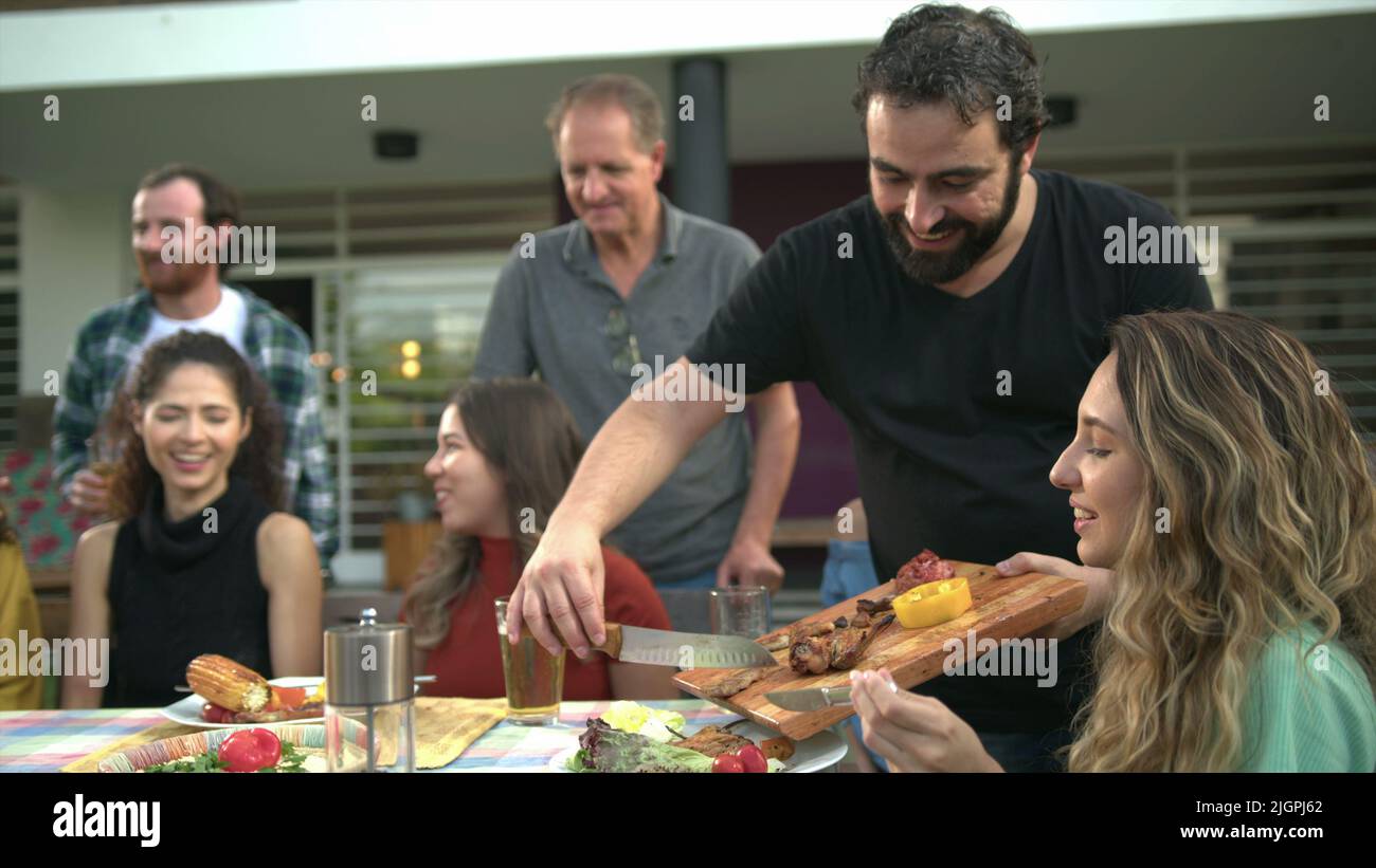 Group of cheerful friends eating barbecue together. BBQ chef serving food to friend. People ...