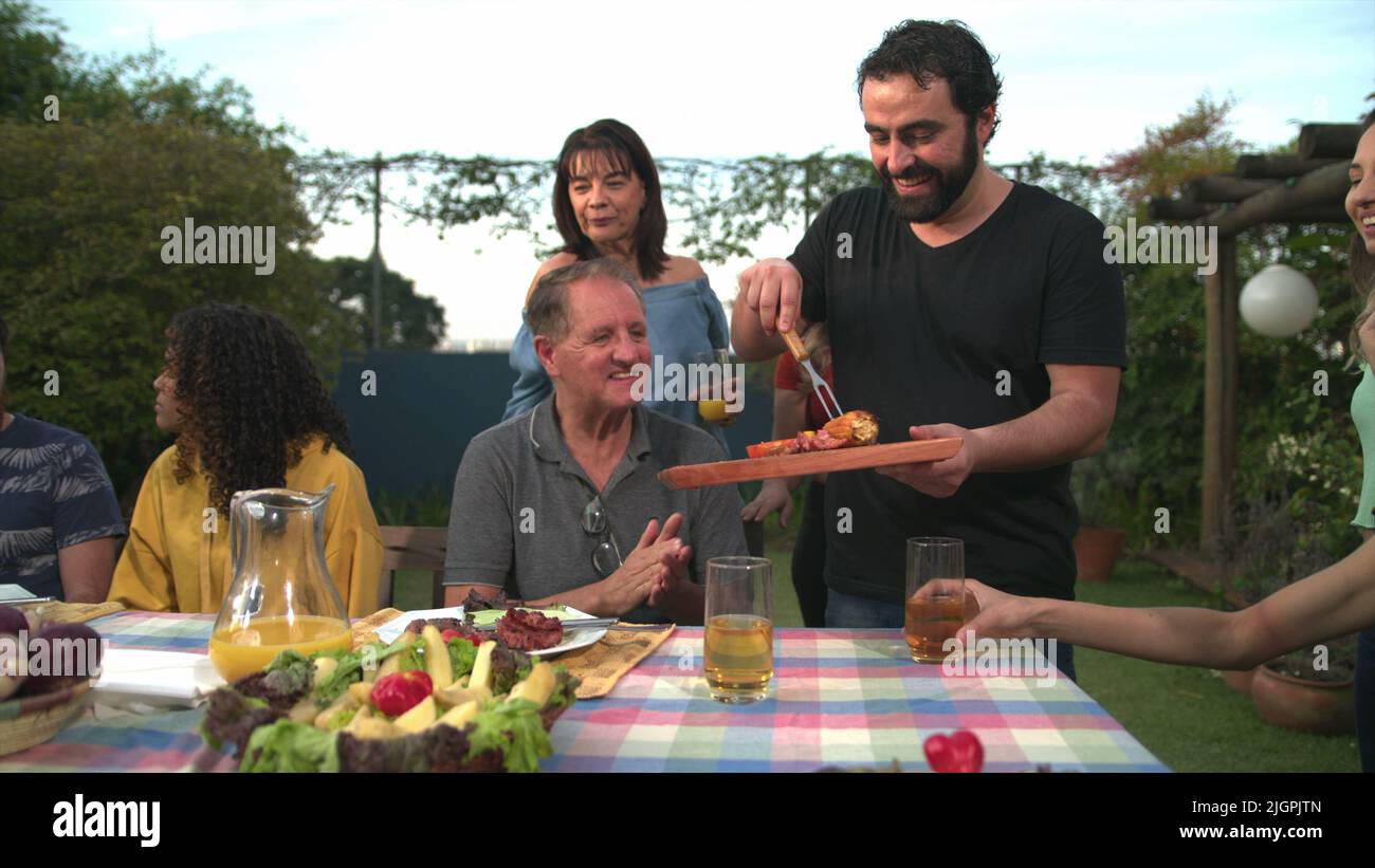 Barbecue chef bringing food to friends and family gathered around table ...