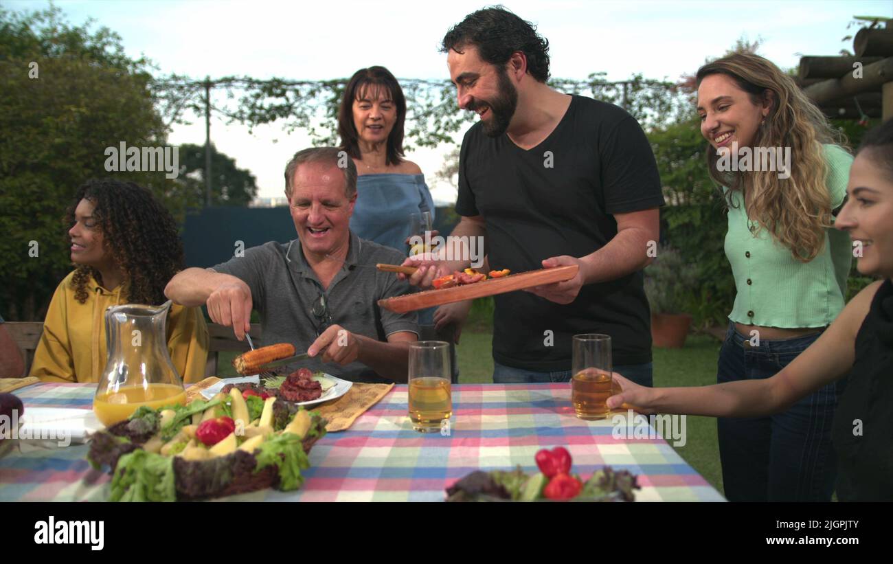 Barbecue chef bringing food to friends and family gathered around table ...
