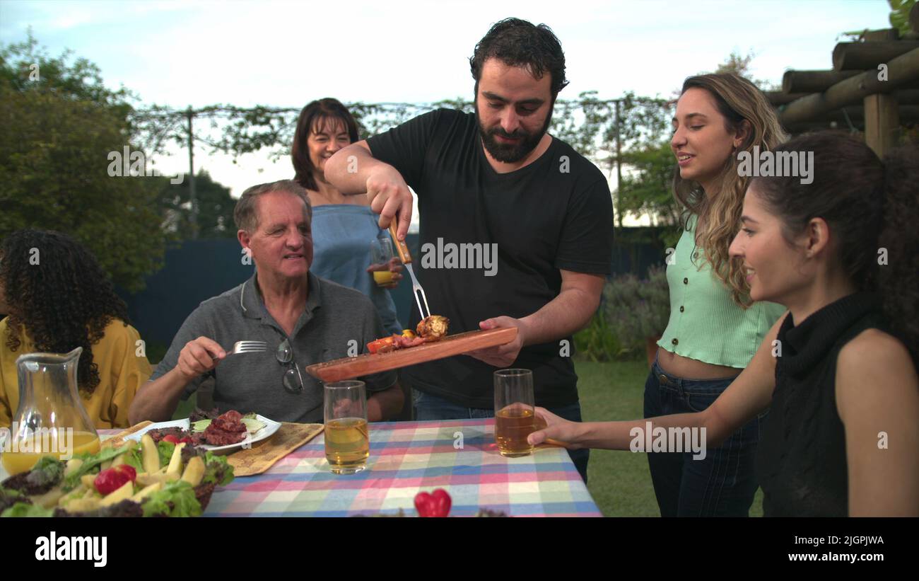 Barbecue chef bringing food to friends and family gathered around table ...