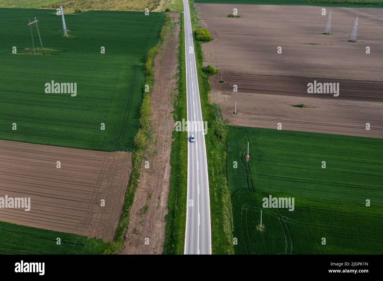 Aerial shot of car driving down the straight road through countryside ...