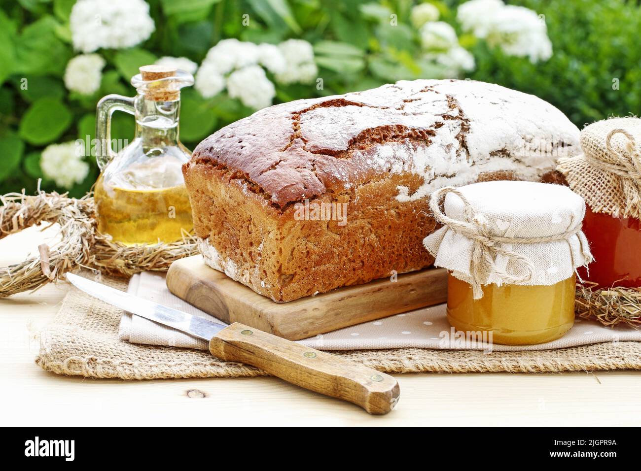 Loaf of bread, jar with honey and summer flowers on the table. Healthy ...