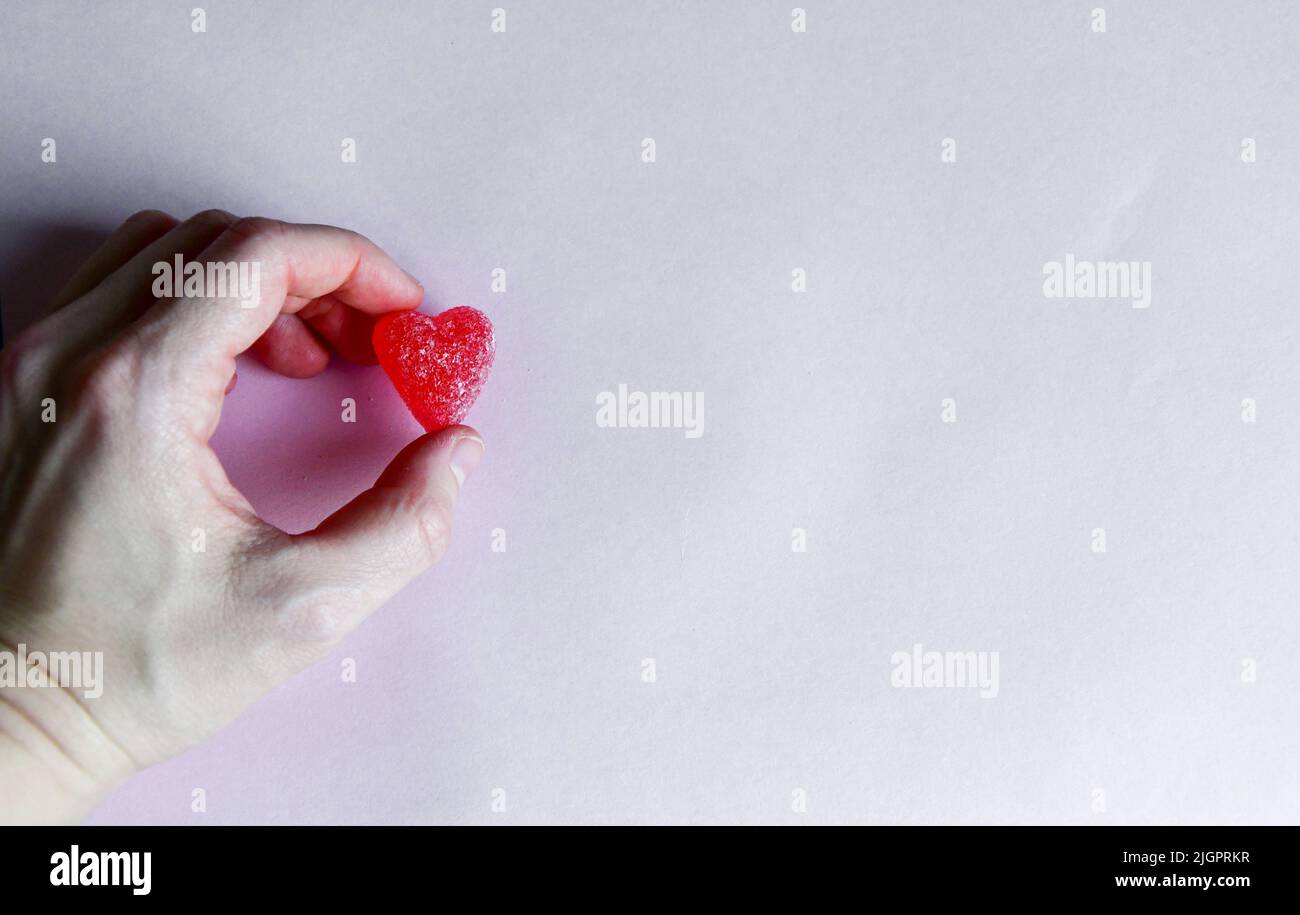 Photo of red jelly candy heart in hand of woman on white background ...