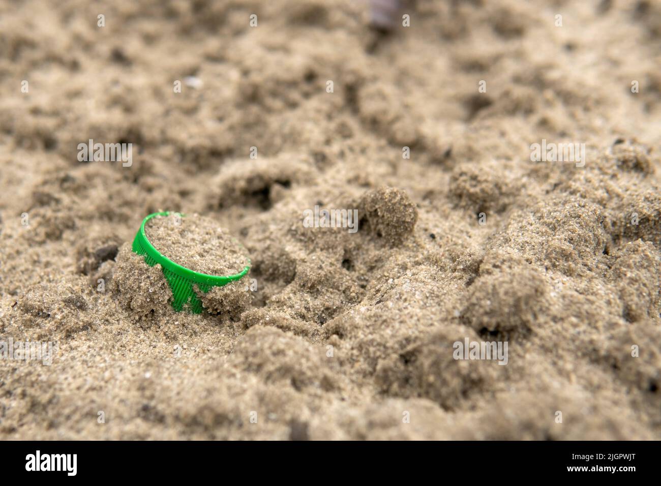 A green cork from a plastic bottle lies in the sand. Environmental ...