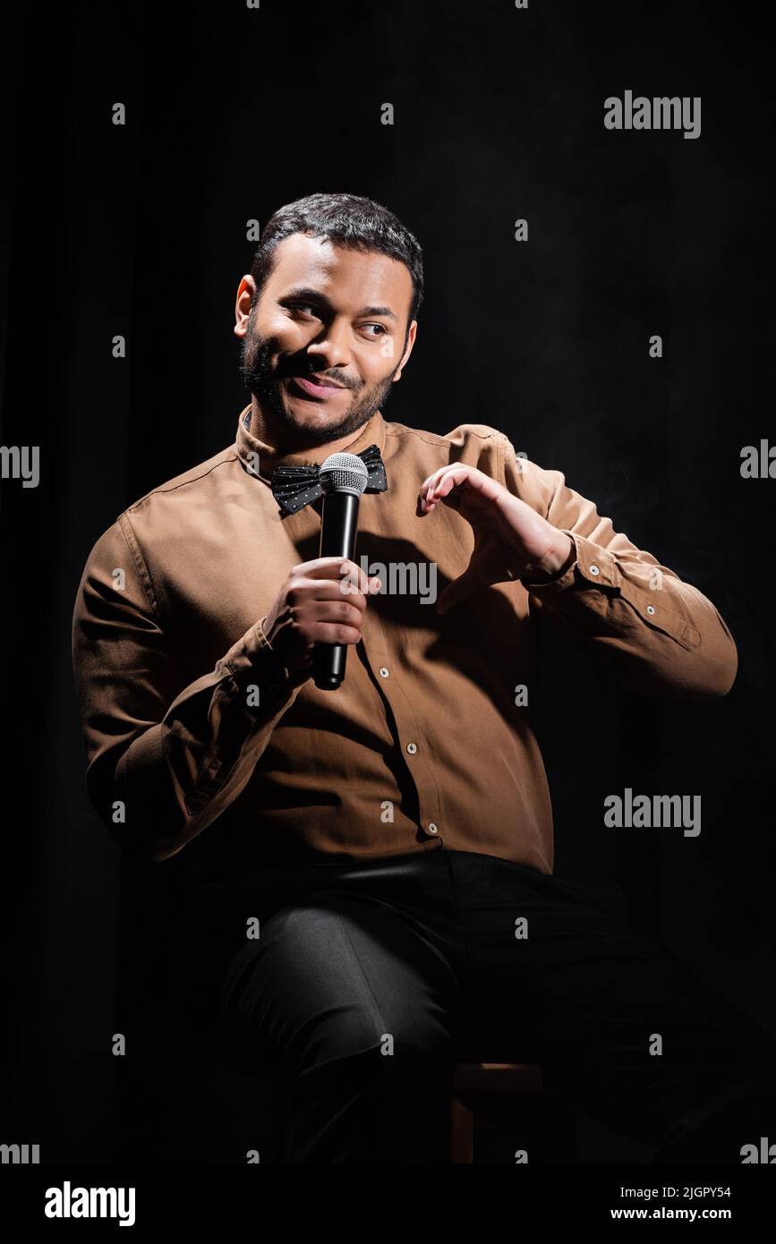 smiling indian comedian sitting and performing stand up comedy on black ...