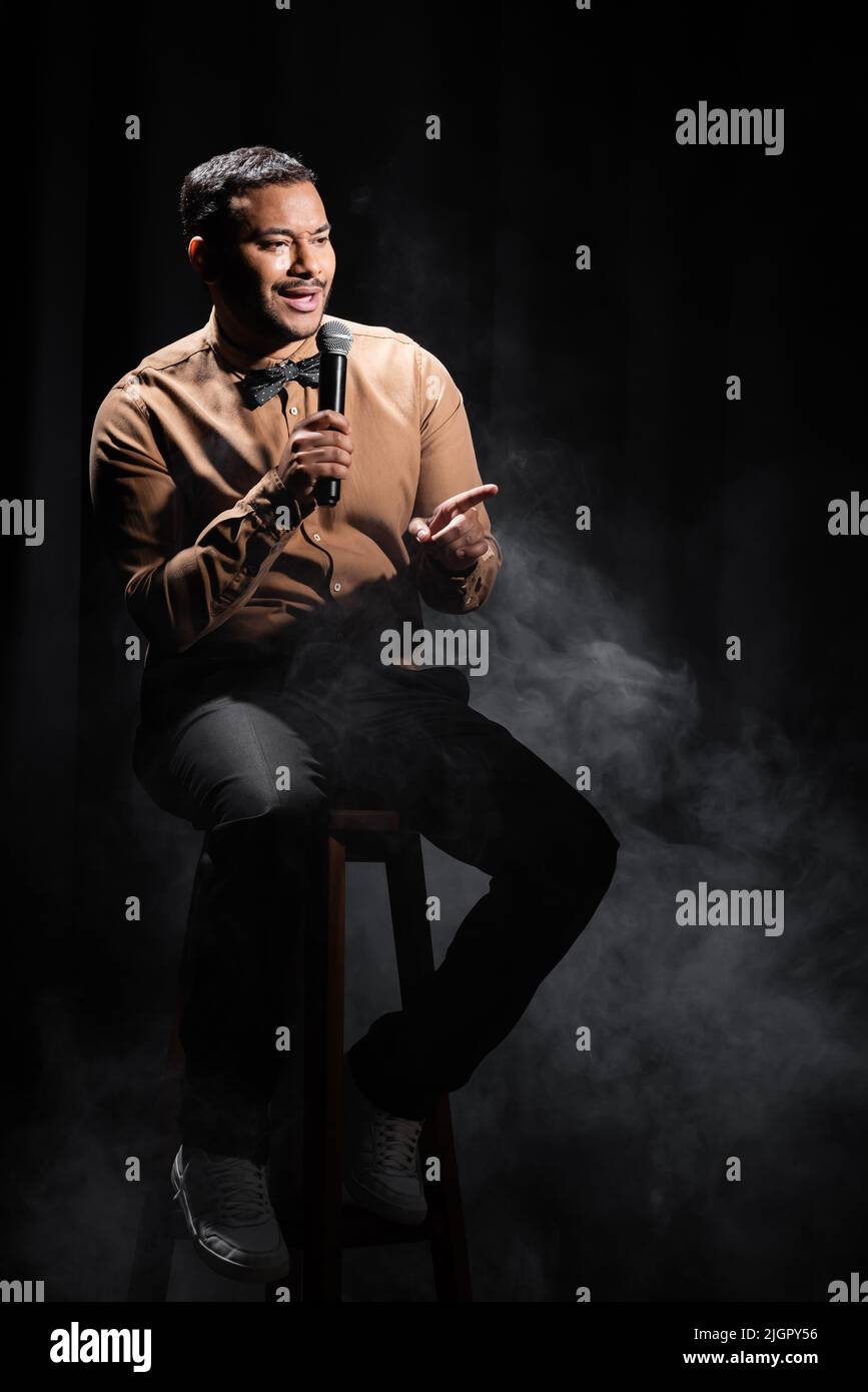 indian comedian sitting and performing stand up comedy into microphone ...