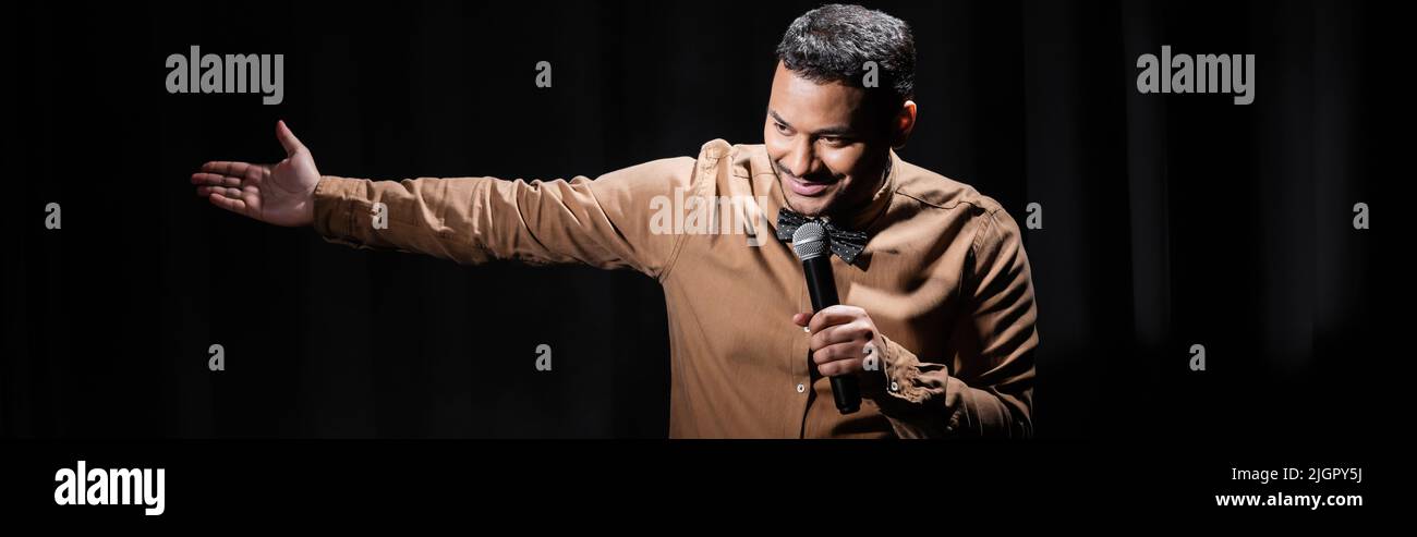smiling indian comedian performing stand up comedy into microphone on ...