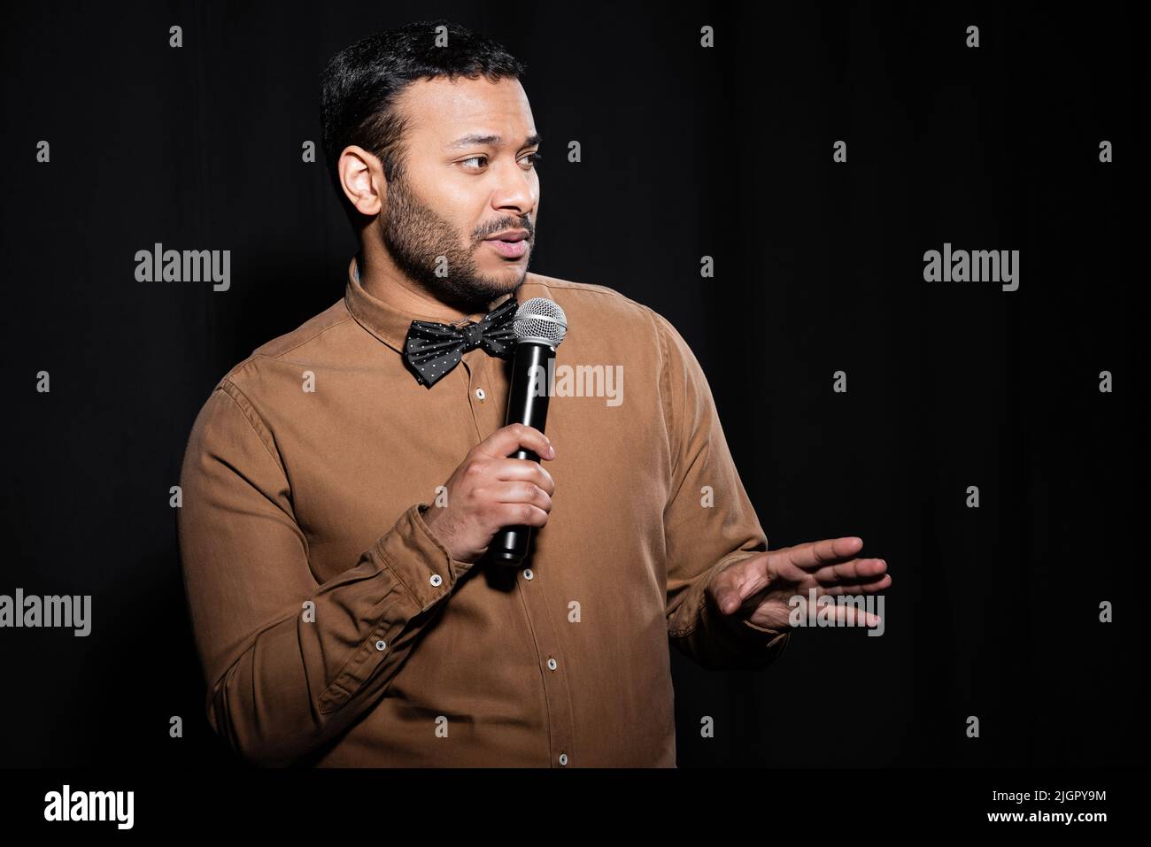 bearded indian stand up comedian in shirt and bow tie holding ...