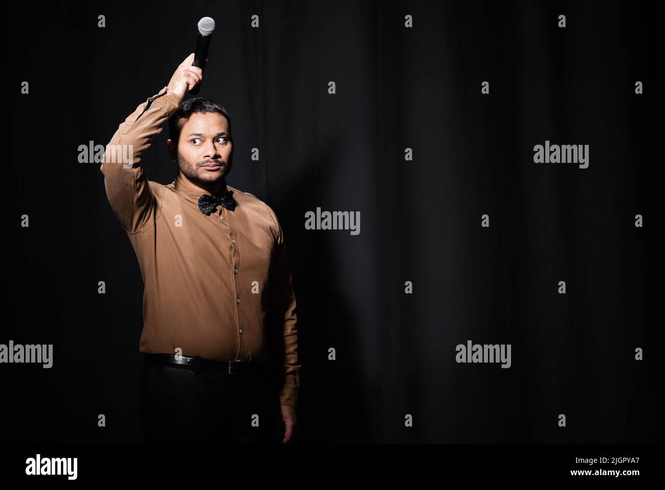 indian stand up comedian holding microphone on head on dark stage on ...