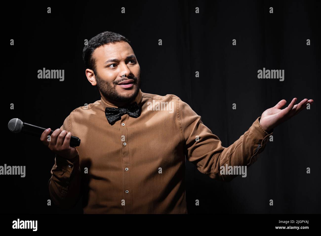 confused indian comedian in shirt and bow tie holding microphone and ...