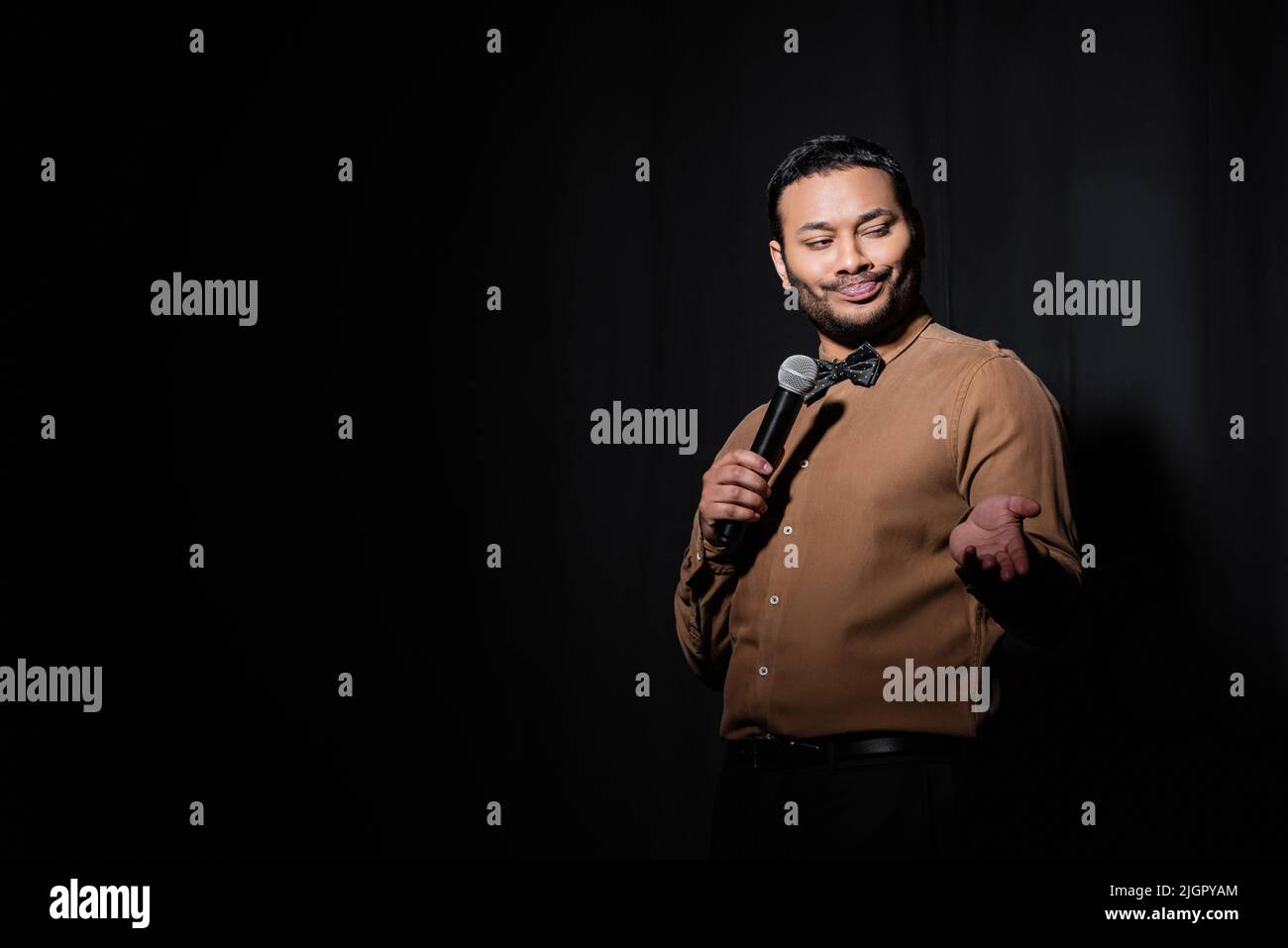 skeptical indian stand up comedian telling joke into microphone on dark ...