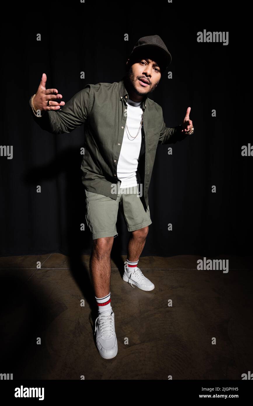 full length of stylish indian hip hop singer in cap gesturing while ...