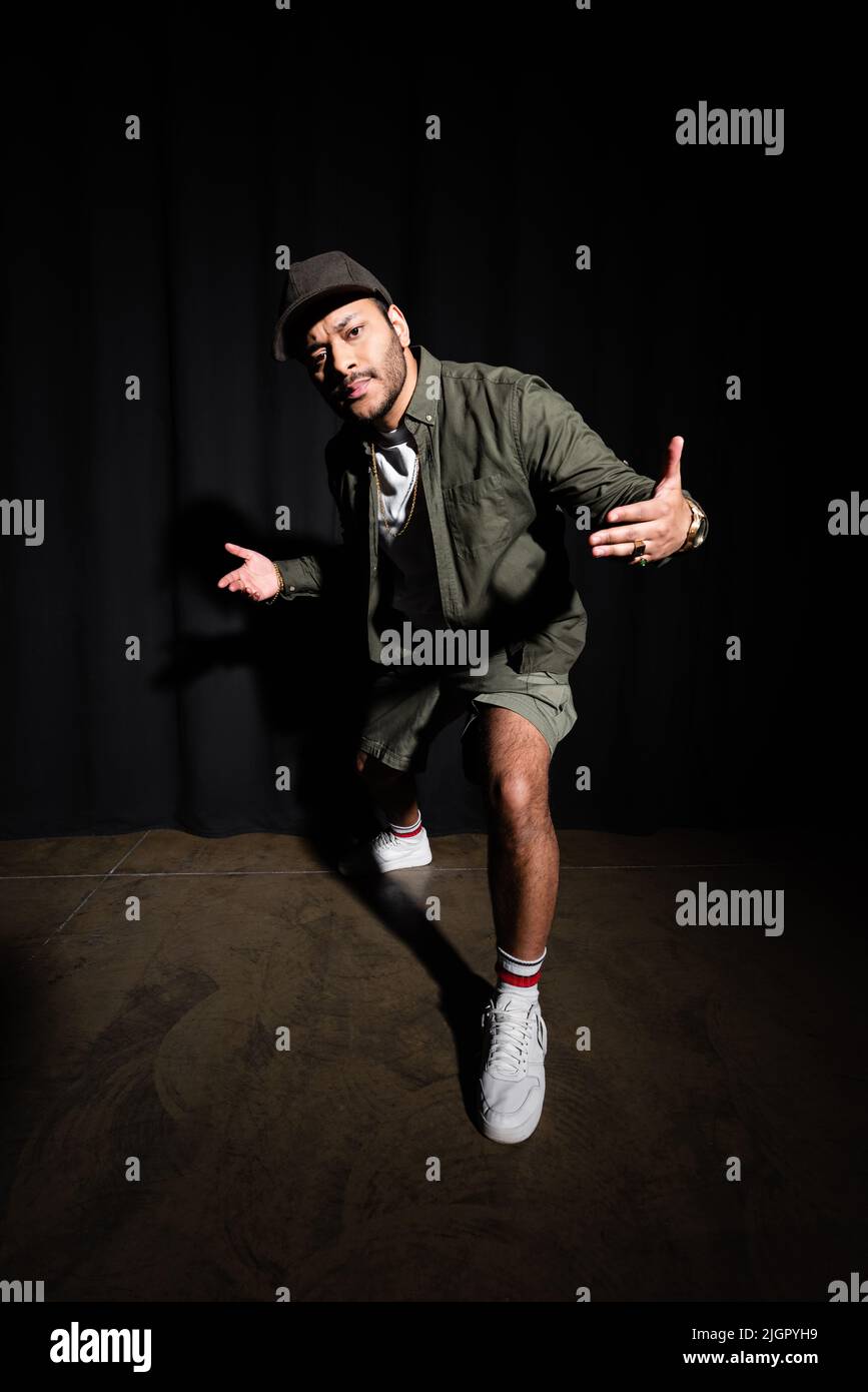 full length of stylish eastern hip hop singer in cap gesturing while ...