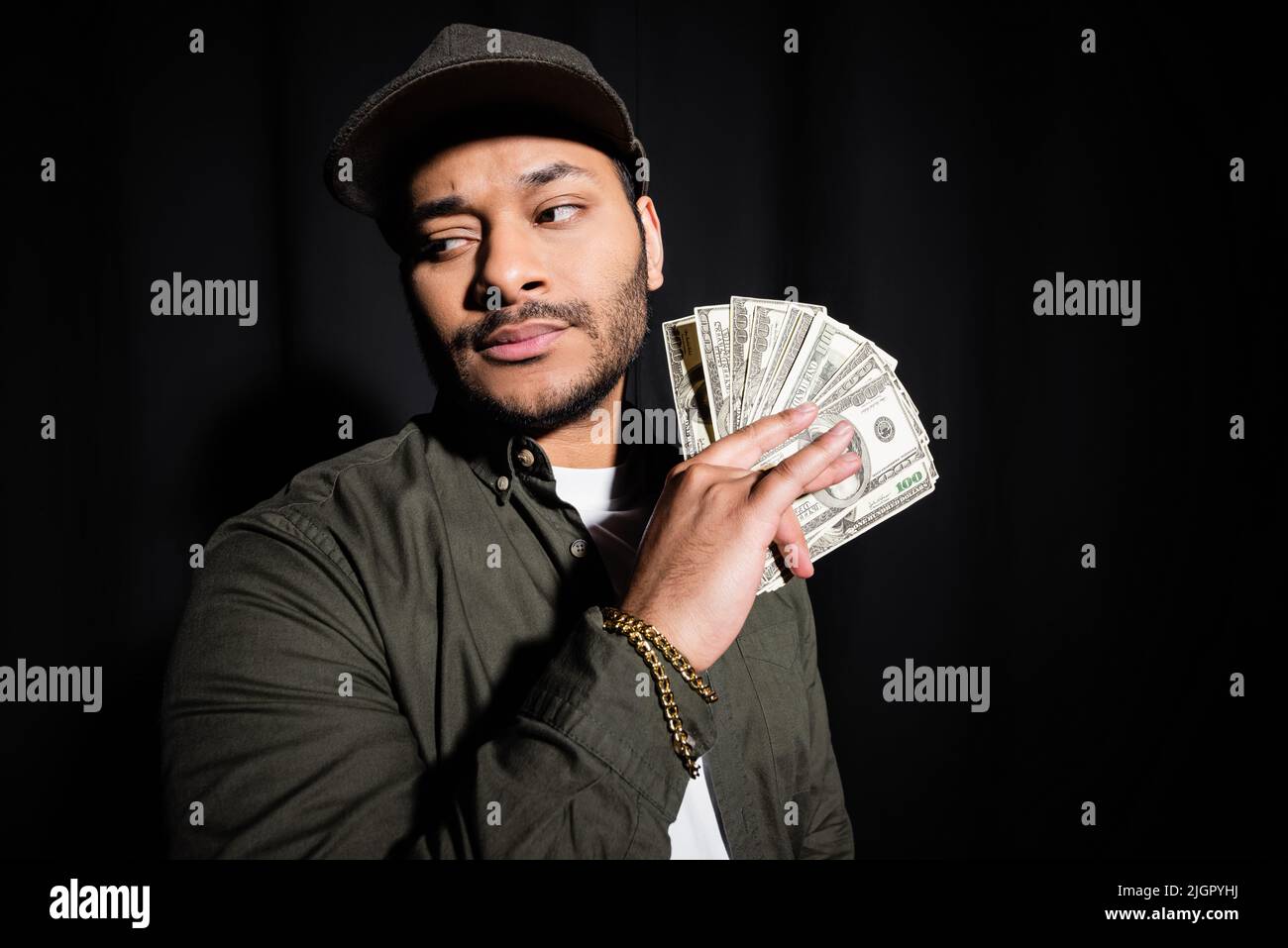 stylish indian hip hop singer in cap holding dollar banknotes isolated ...