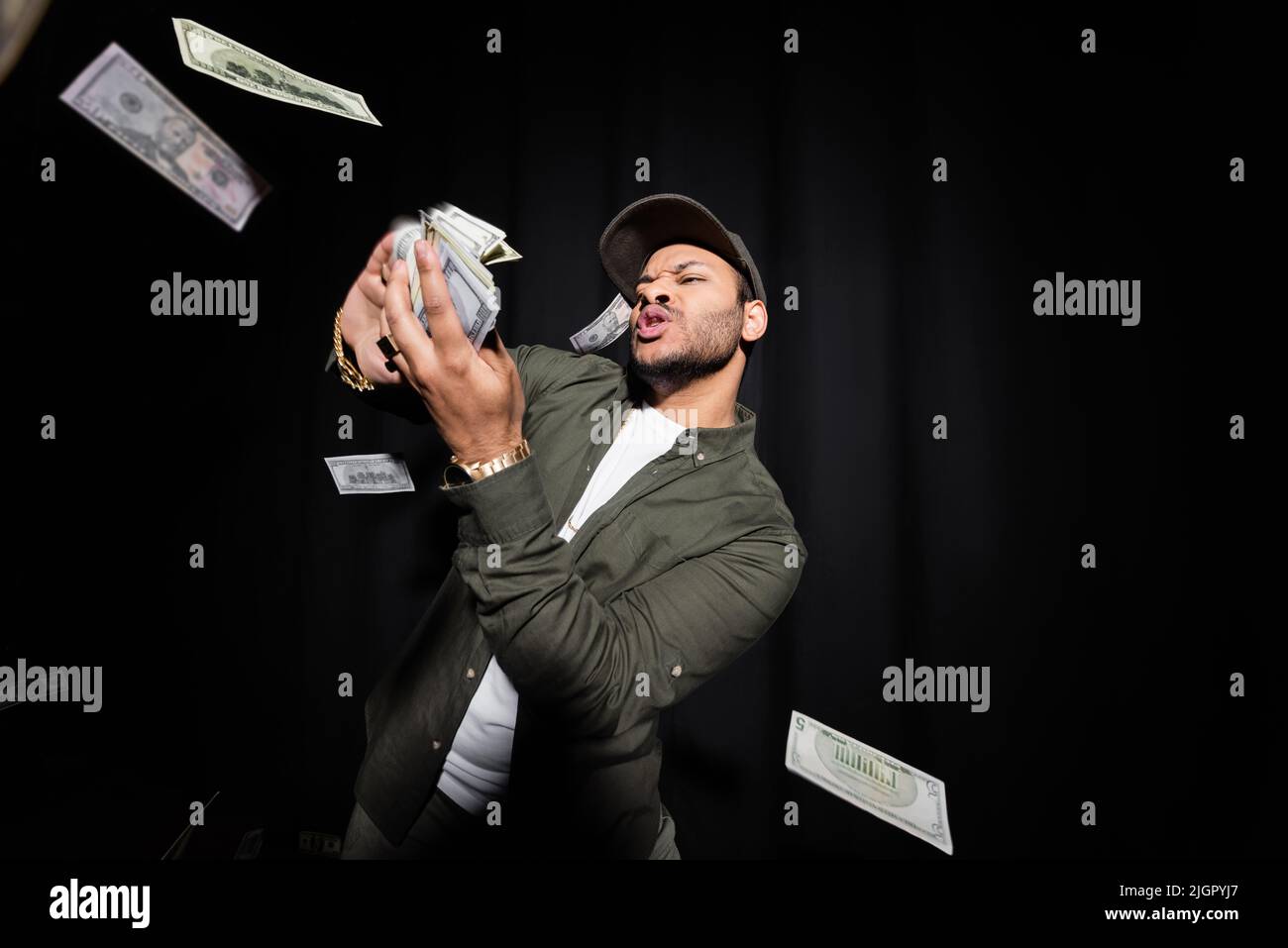 rich indian hip hop performer in cap throwing blurred dollar banknotes ...